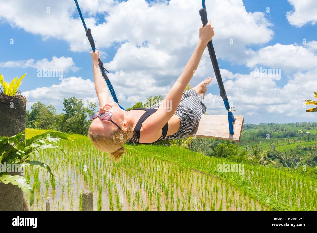 Happy sporty female traveller swinging on wooden swing, enjoying summer ...
