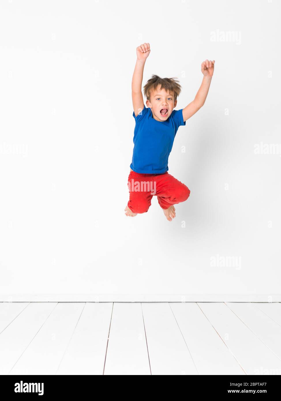 cool, cute boy with blue shirt and red trousers is jumping high in the ...