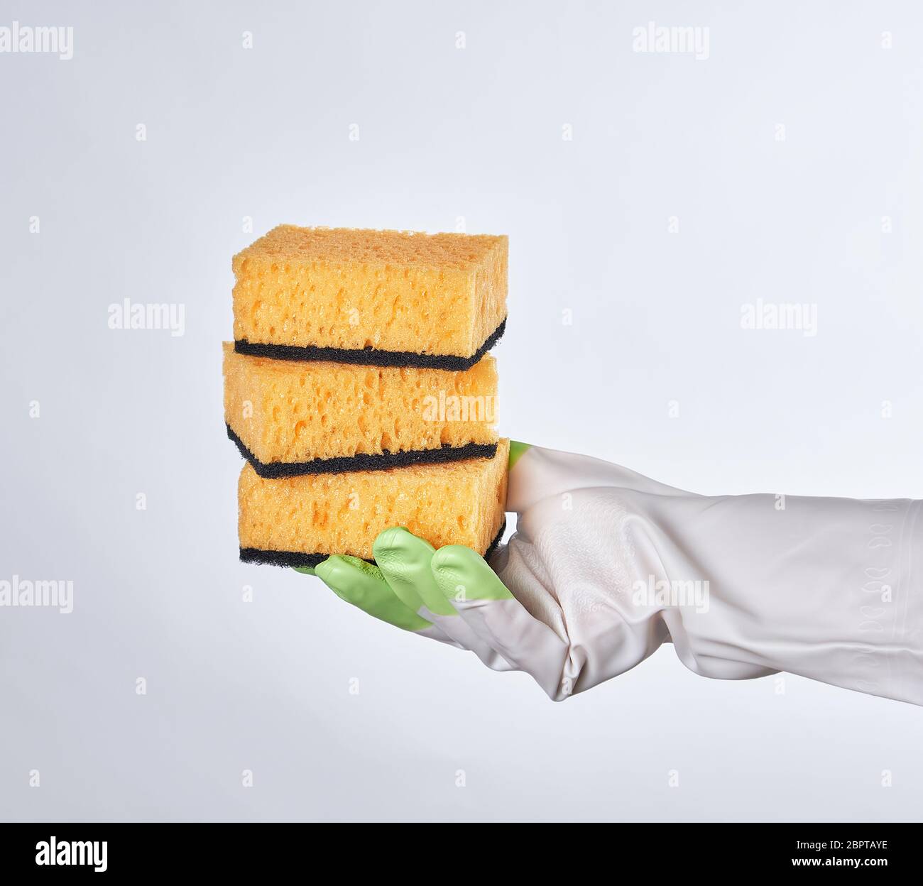 gloved hand holds yellow kitchen sponge, white background Stock Photo ...