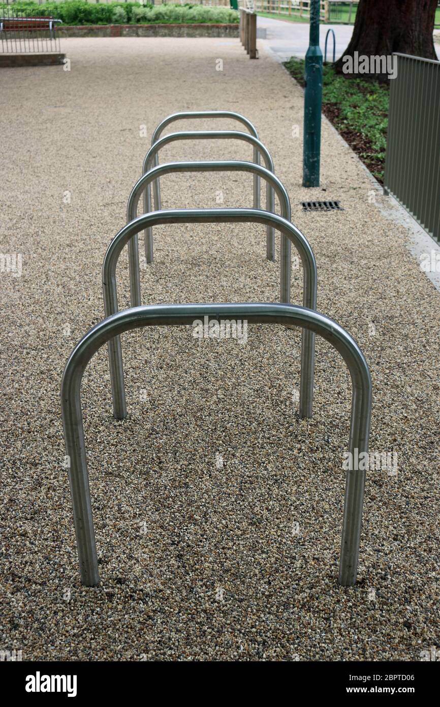 Five metal new bicycle racks on a gravel surfaced tarmac path in a park ...
