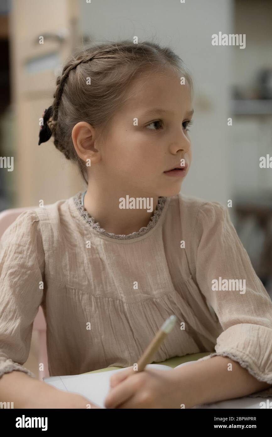 A dark blond girl in a beige dress is doing homework Stock Photo - Alamy