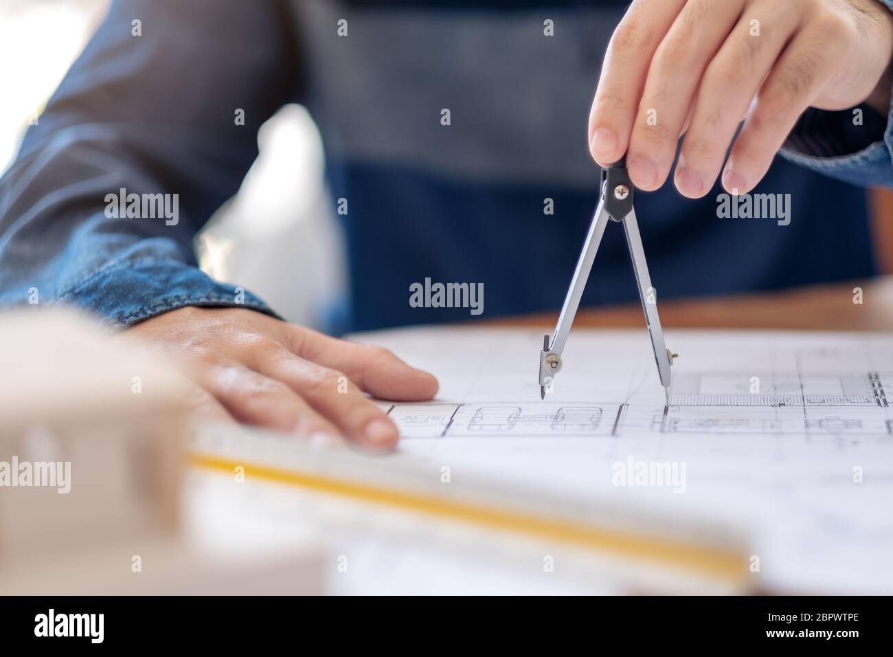An architect using compass to draw and measure shop drawing in office ...