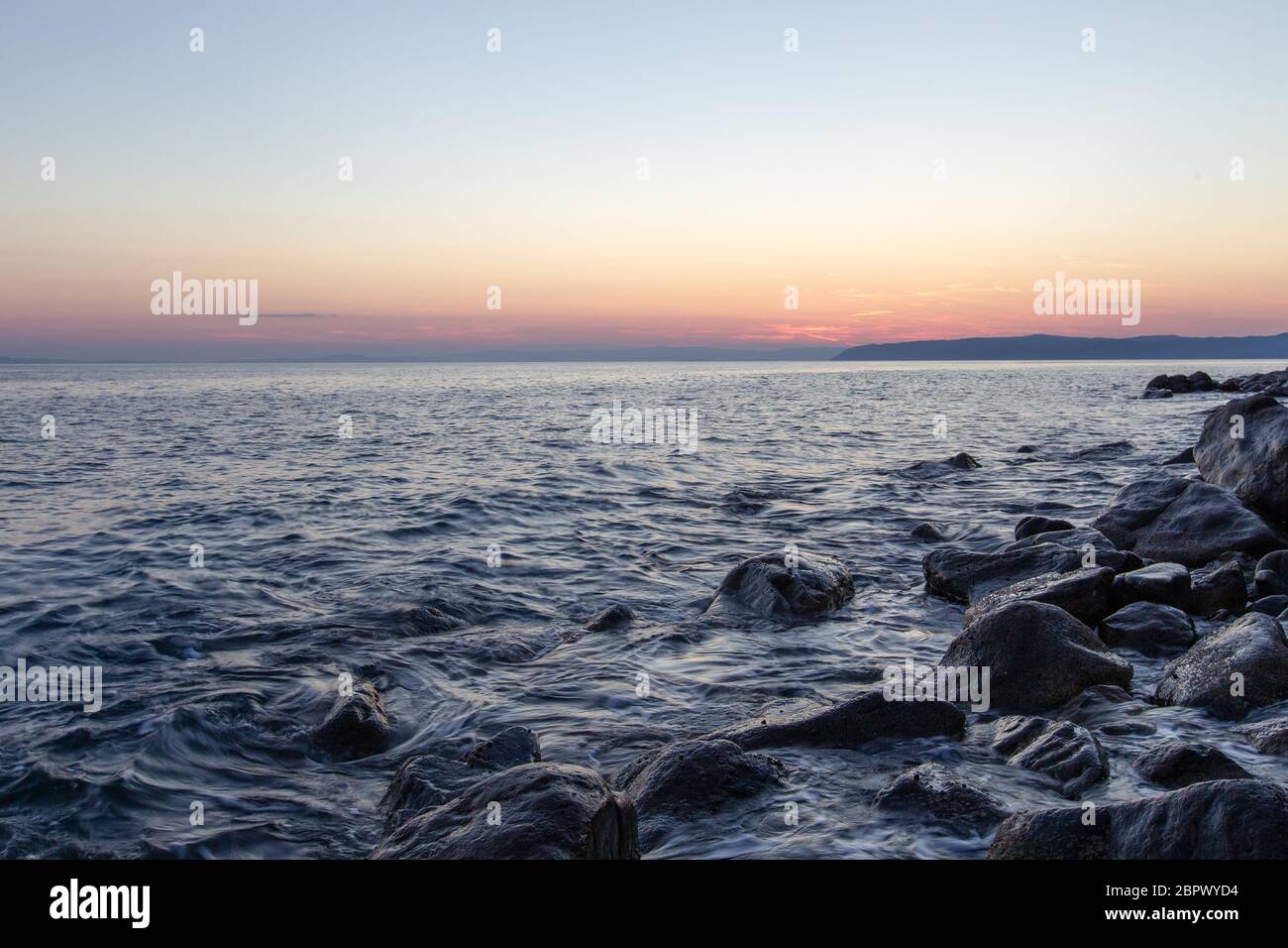 The sea wave hits the stones at sunset near the coast of the Holy Mount ...
