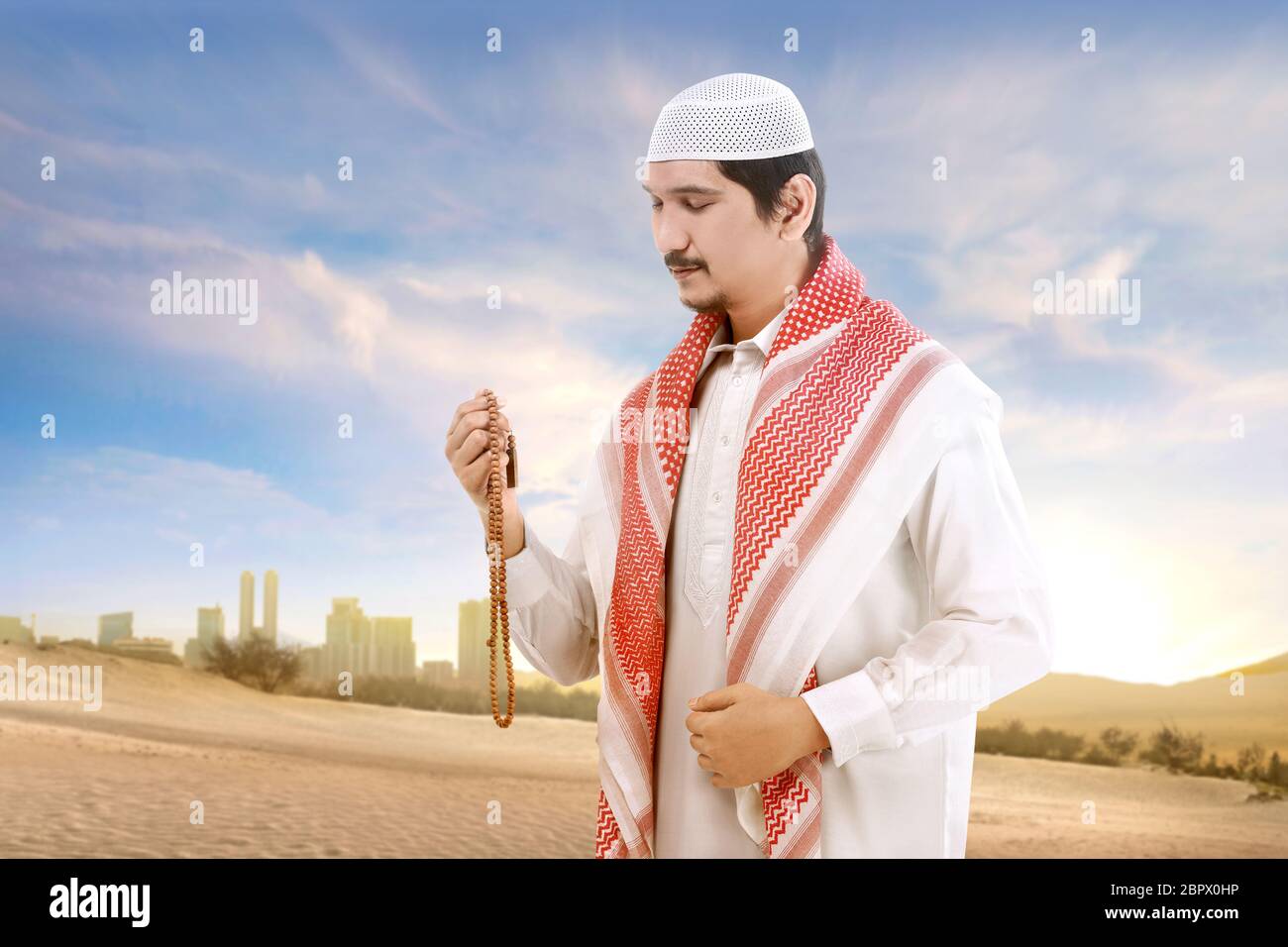 Young asian muslim man with cap and turban standing and praying with ...