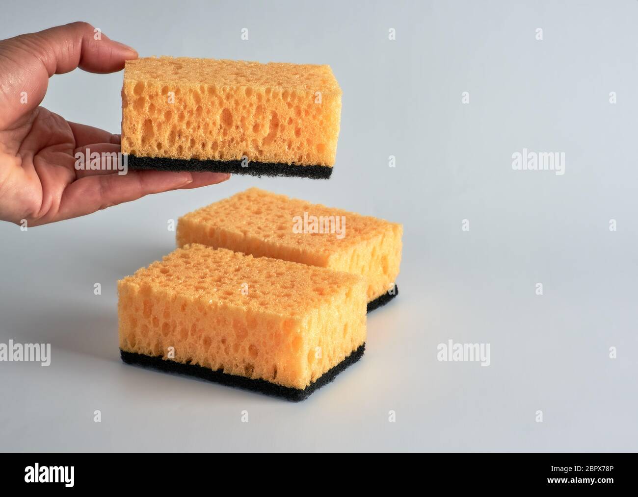 hand is holding a yellow kitchen sponge for washing dishes on a white ...