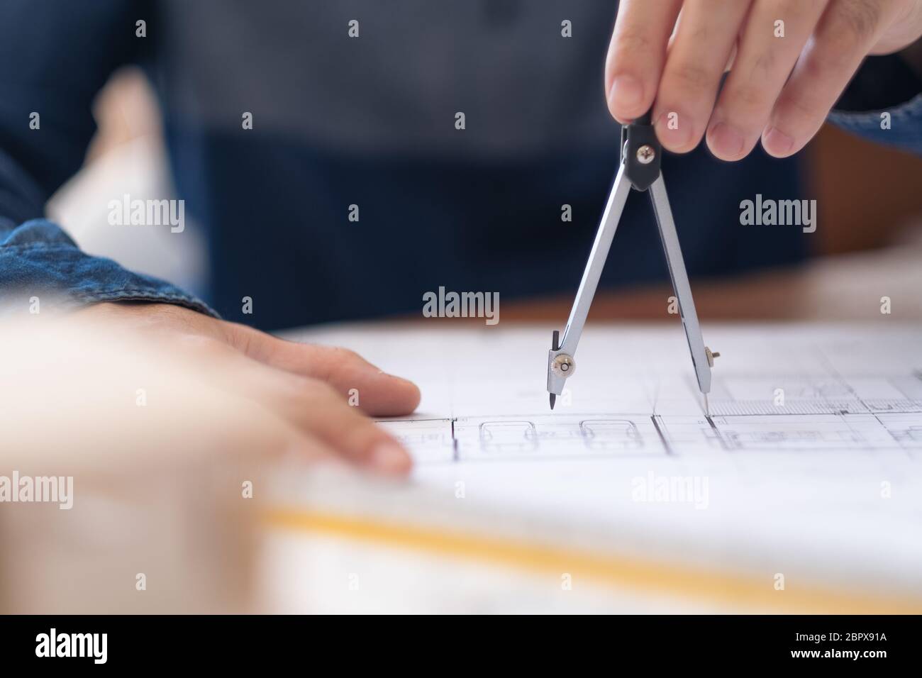 An architect using compass to draw and measure shop drawing in office ...