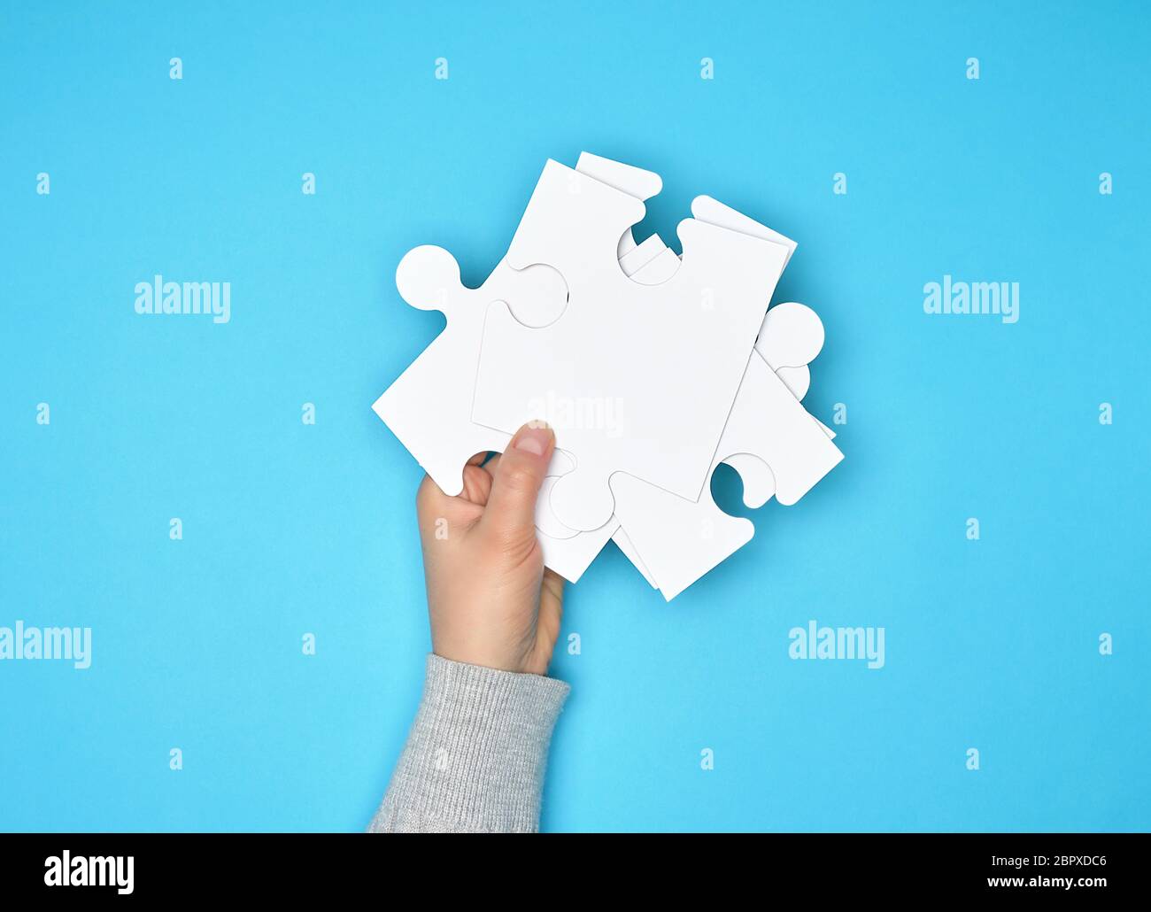 female hand holding a stack of large white paper puzzles on a blue ...