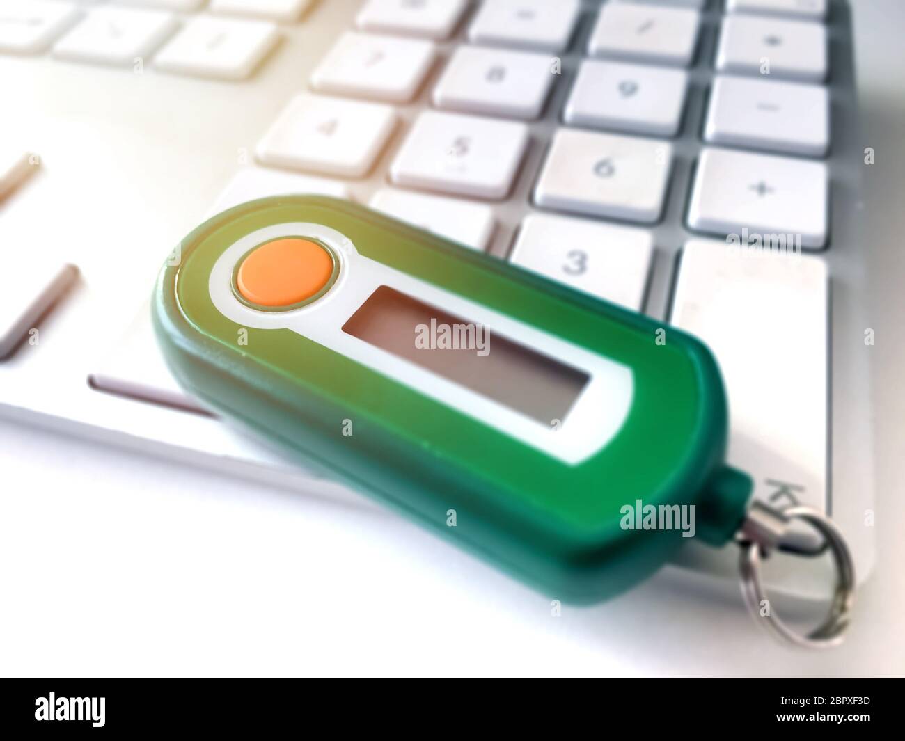 Male hand holding a bank code generator on a white computer keyboard ...