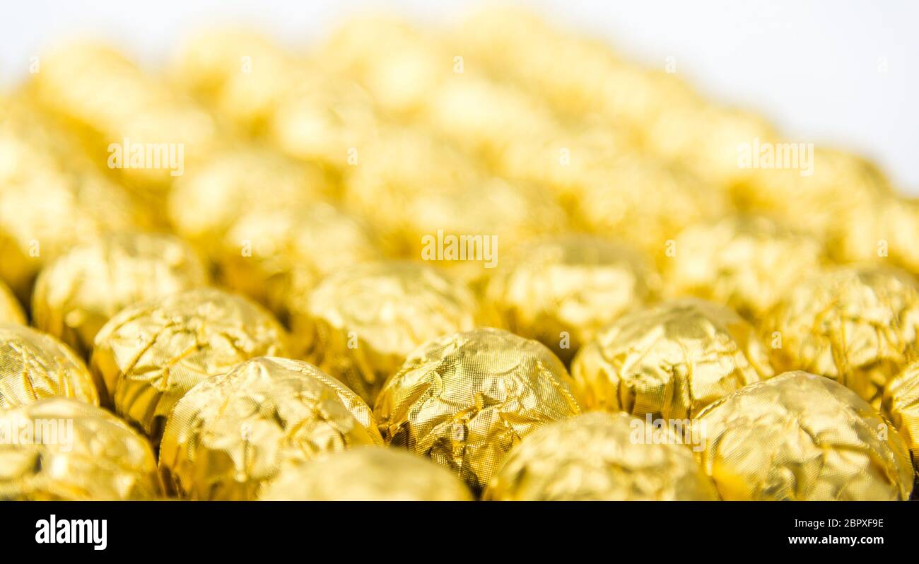 a lot of shiny golden chocolate wrapper in line on white background ...