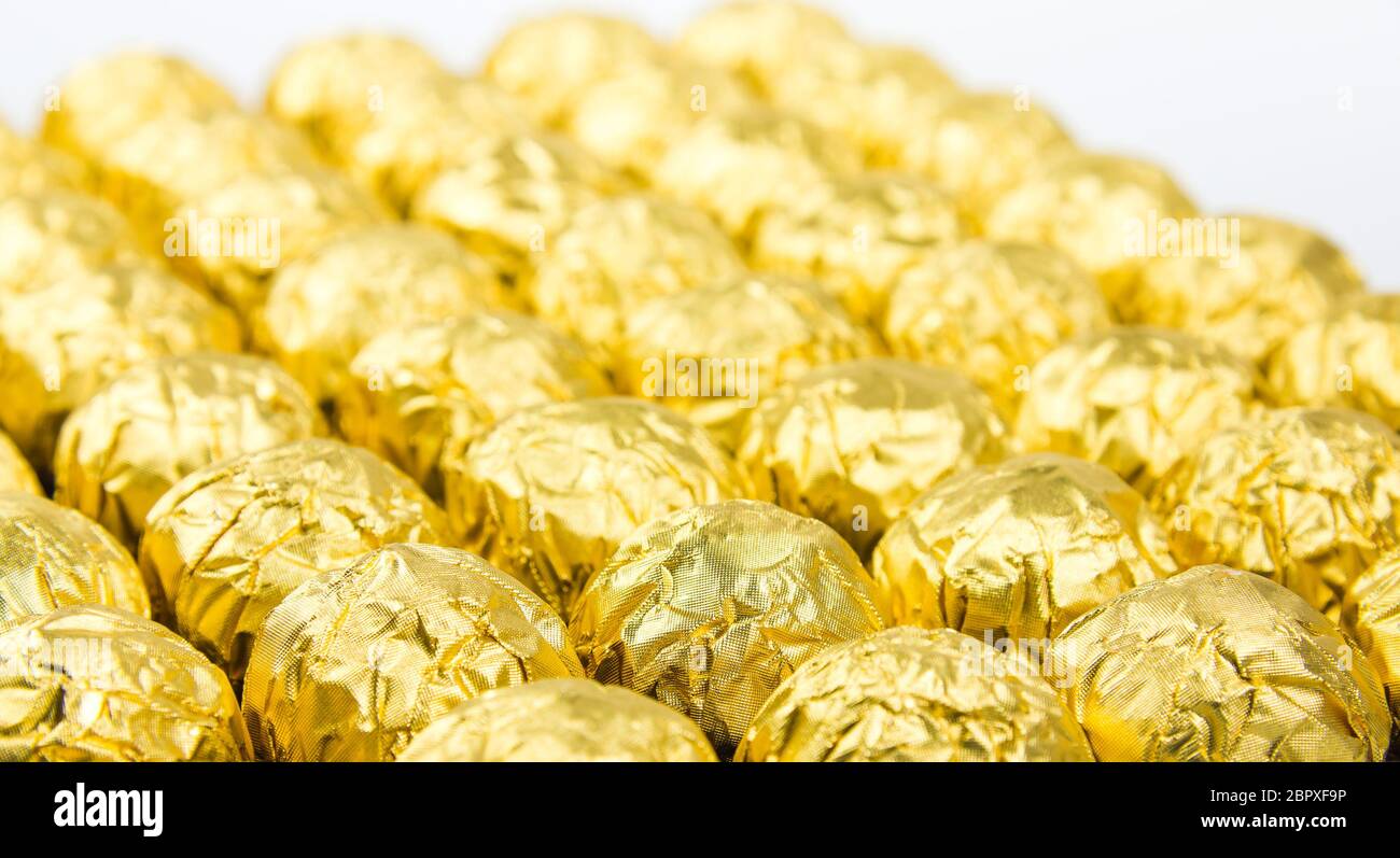 a lot of shiny golden chocolate wrapper in line on white background ...