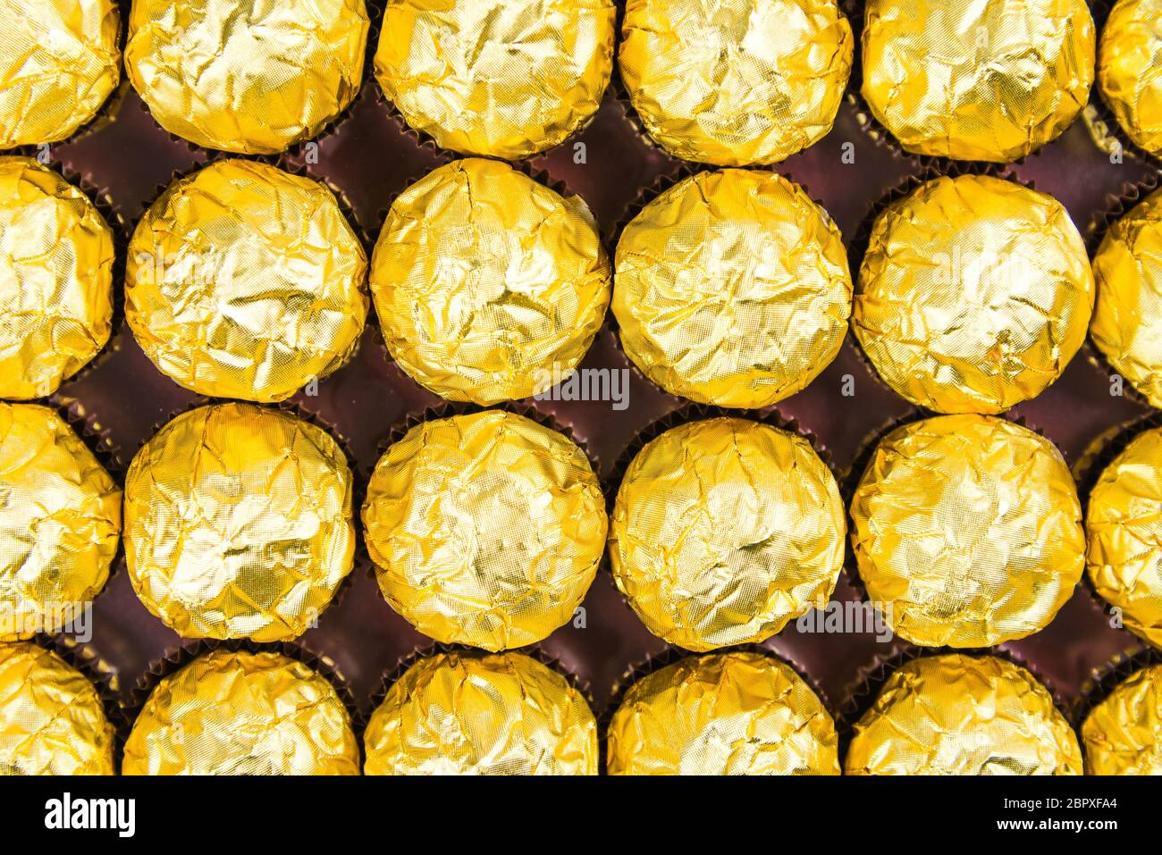 a lot of shiny golden chocolate wrapper in line on white background ...