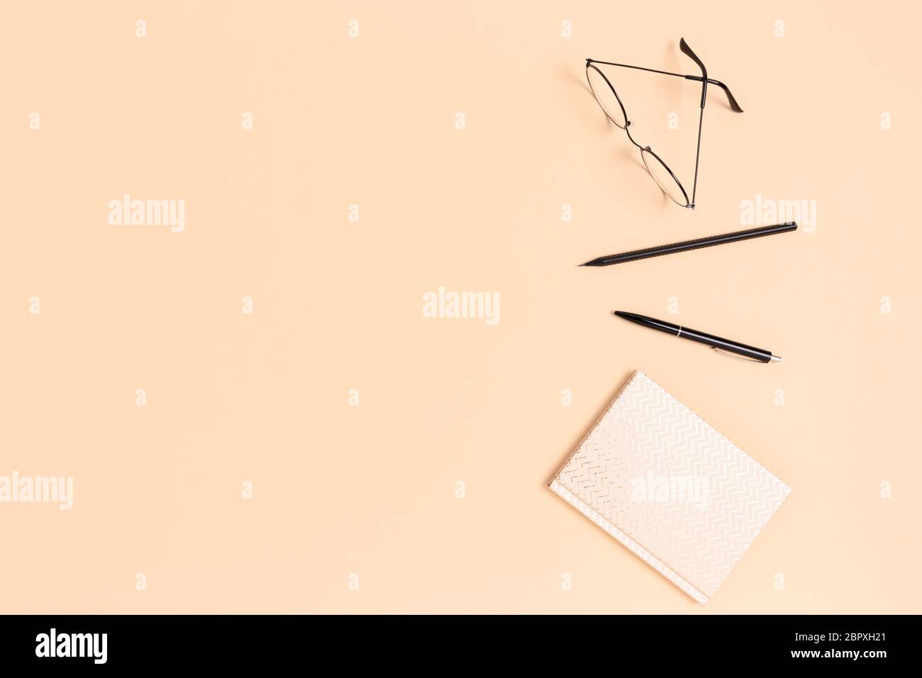 Top view of glasses, pencil, pen and golden notepad on a beige ...