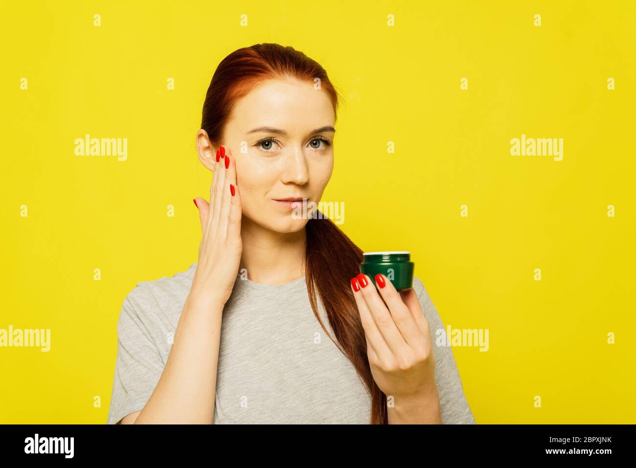 A red head girl is applying cream on the face . A girl smears face ...