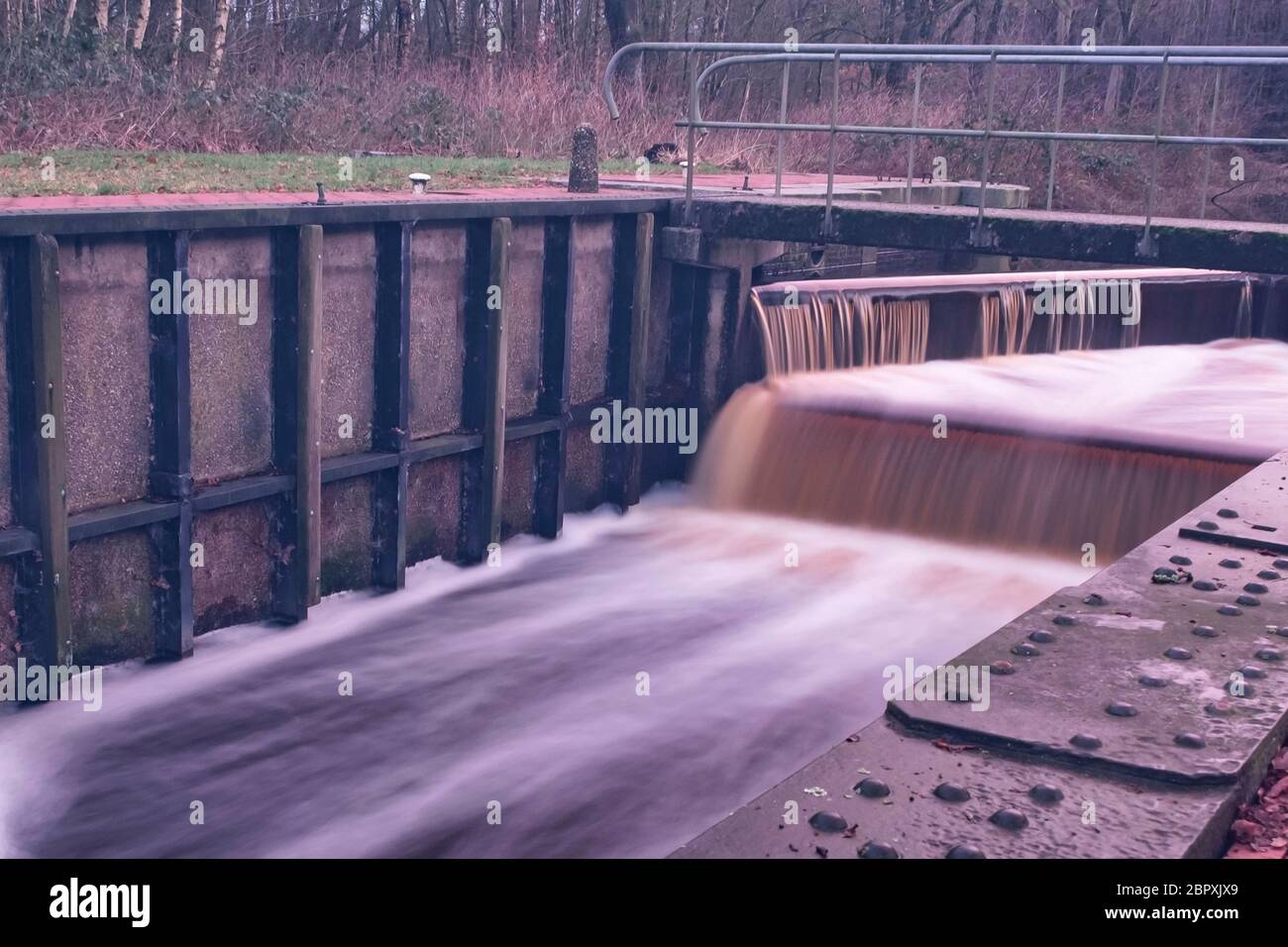 In a weir a lot of water flows along the weir, reflection of trees in ...