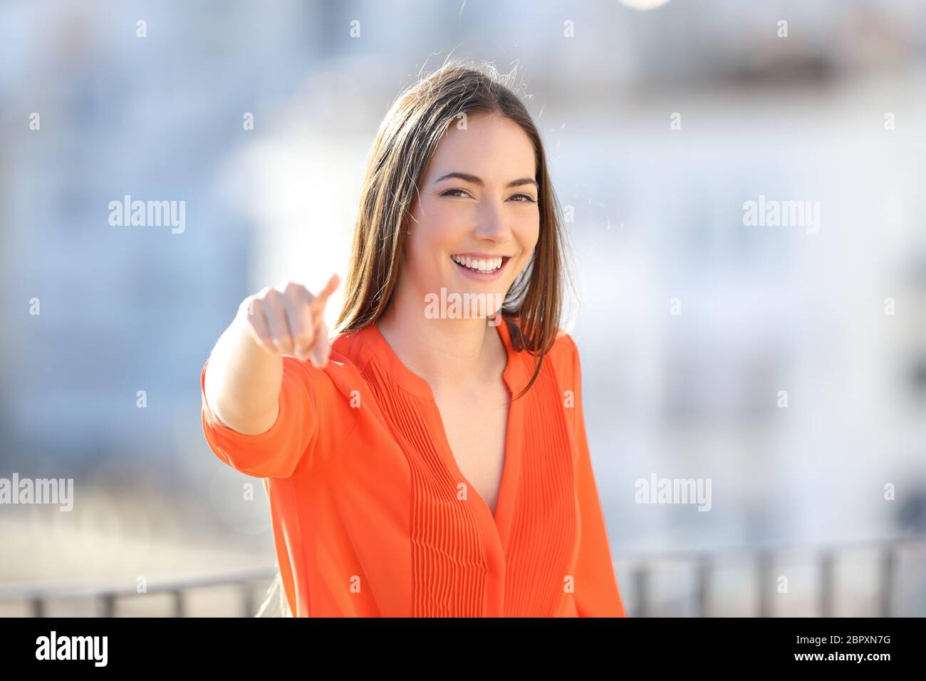 Happy woman in orange pointing at camera in a town outskirts a sunny ...