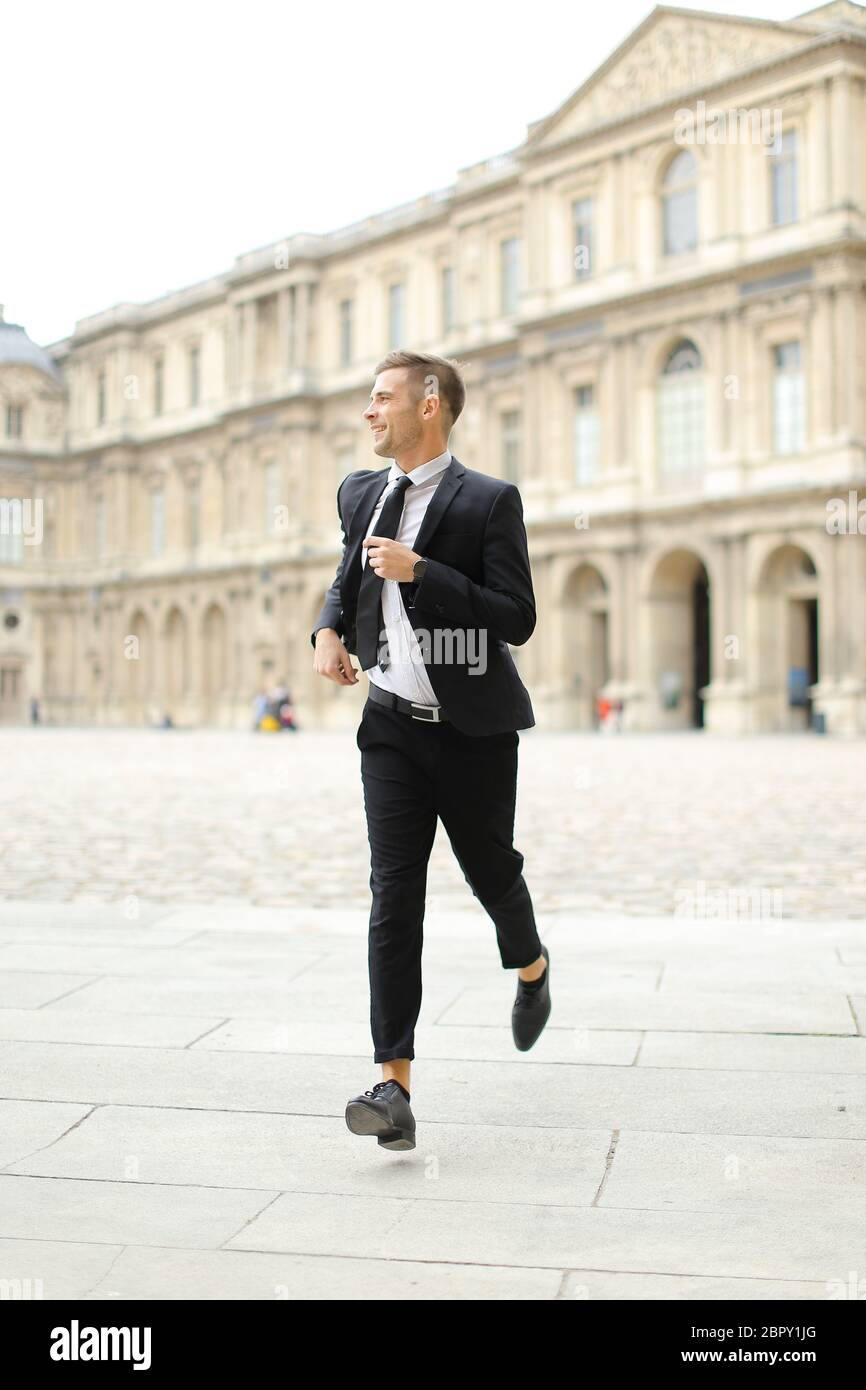 Young man wearing black suit running in Paris, building in background ...