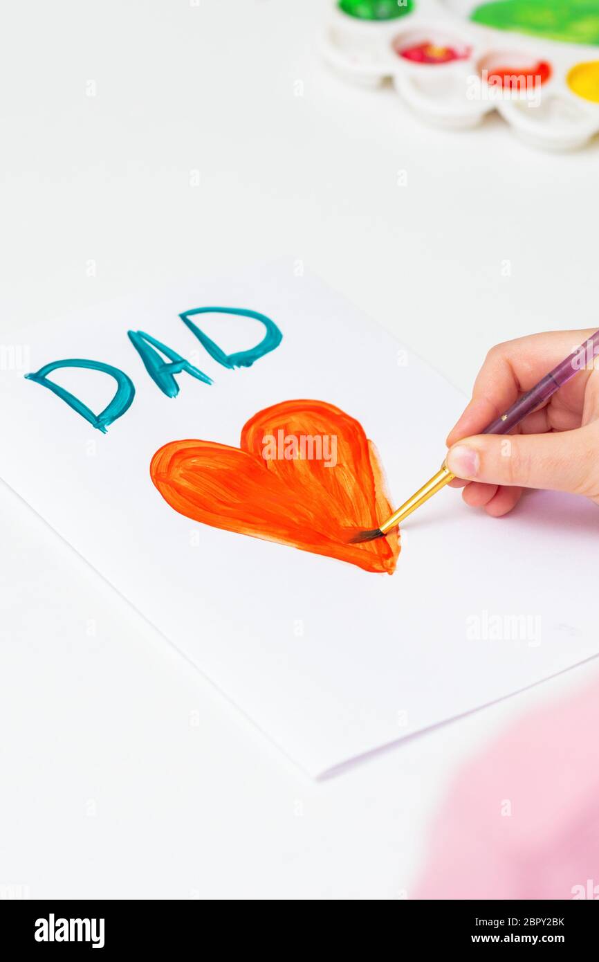 Hand of child drawing red heart with word Dad greeting card on white ...