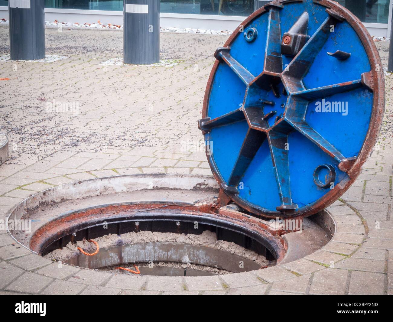 Open heavy manhole cover with blue inside on a sidewalk in front of ...