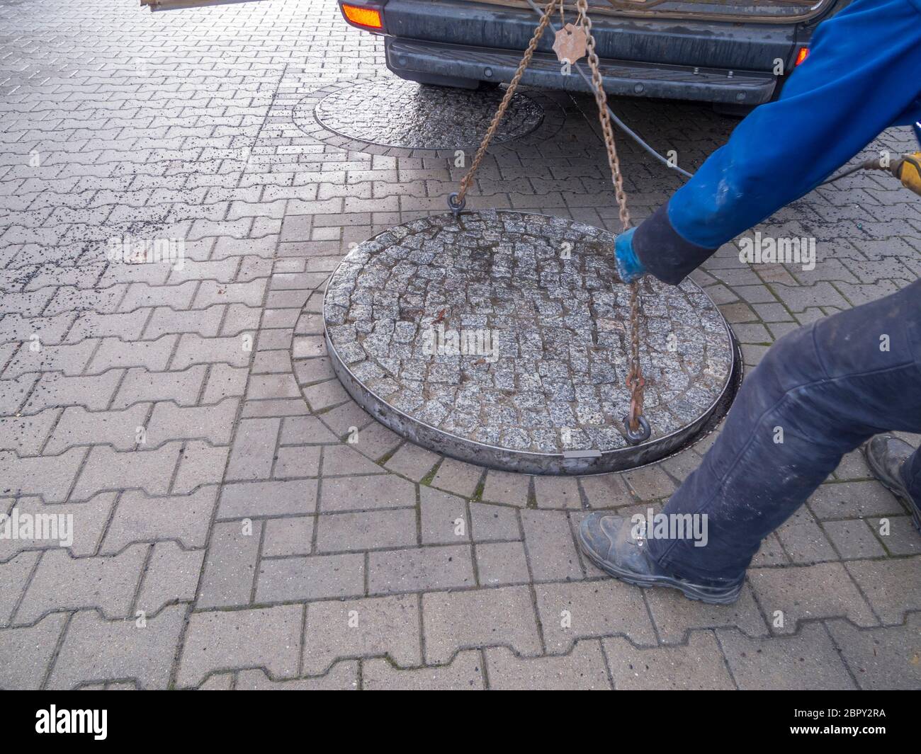 Unrecognizable municipal utility worker opening a heavy double manhole ...