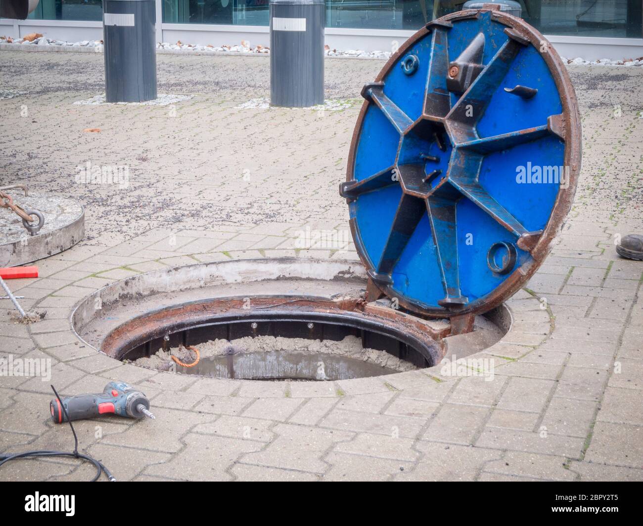 Open heavy manhole cover with blue inside and surrounding tools on a ...