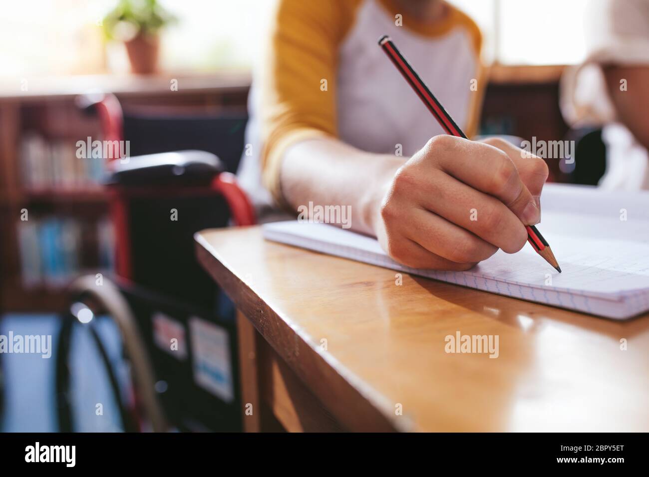Close up of female student taking notes sitting in wheelchair at desk ...