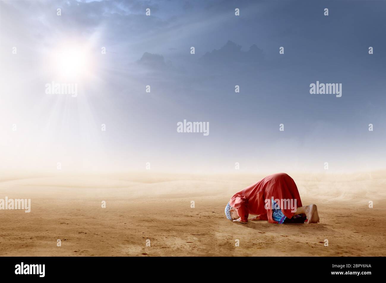 Rear view of asian muslim man praying in prostration position on desert ...