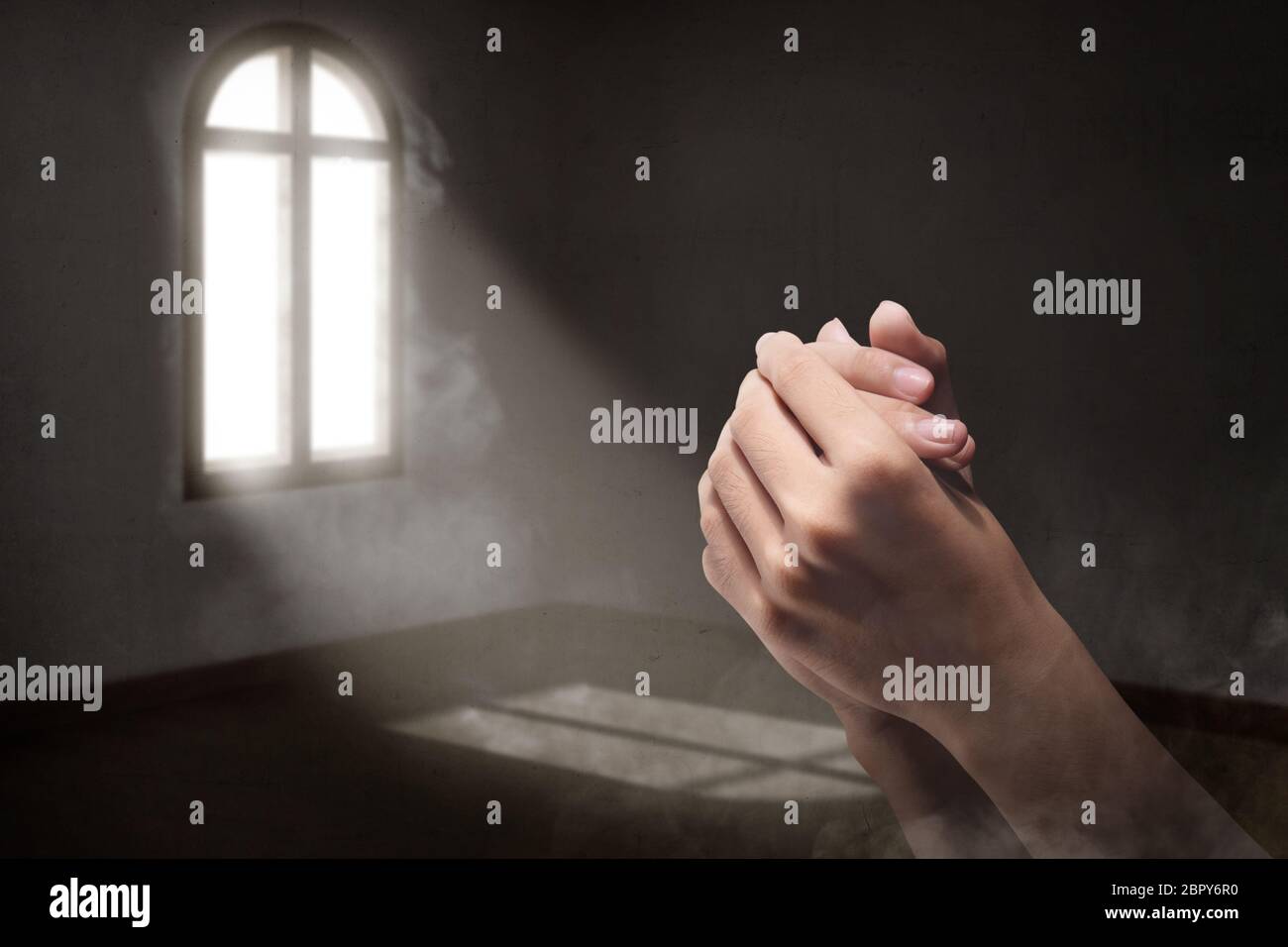 Male hands in praying position inside the room with light from outside ...