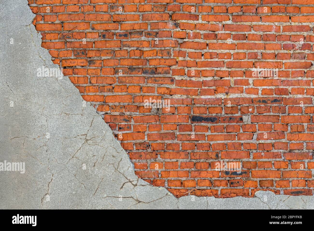 old bad brick wall with leftovers of gray peeled thick sandy plaster ...