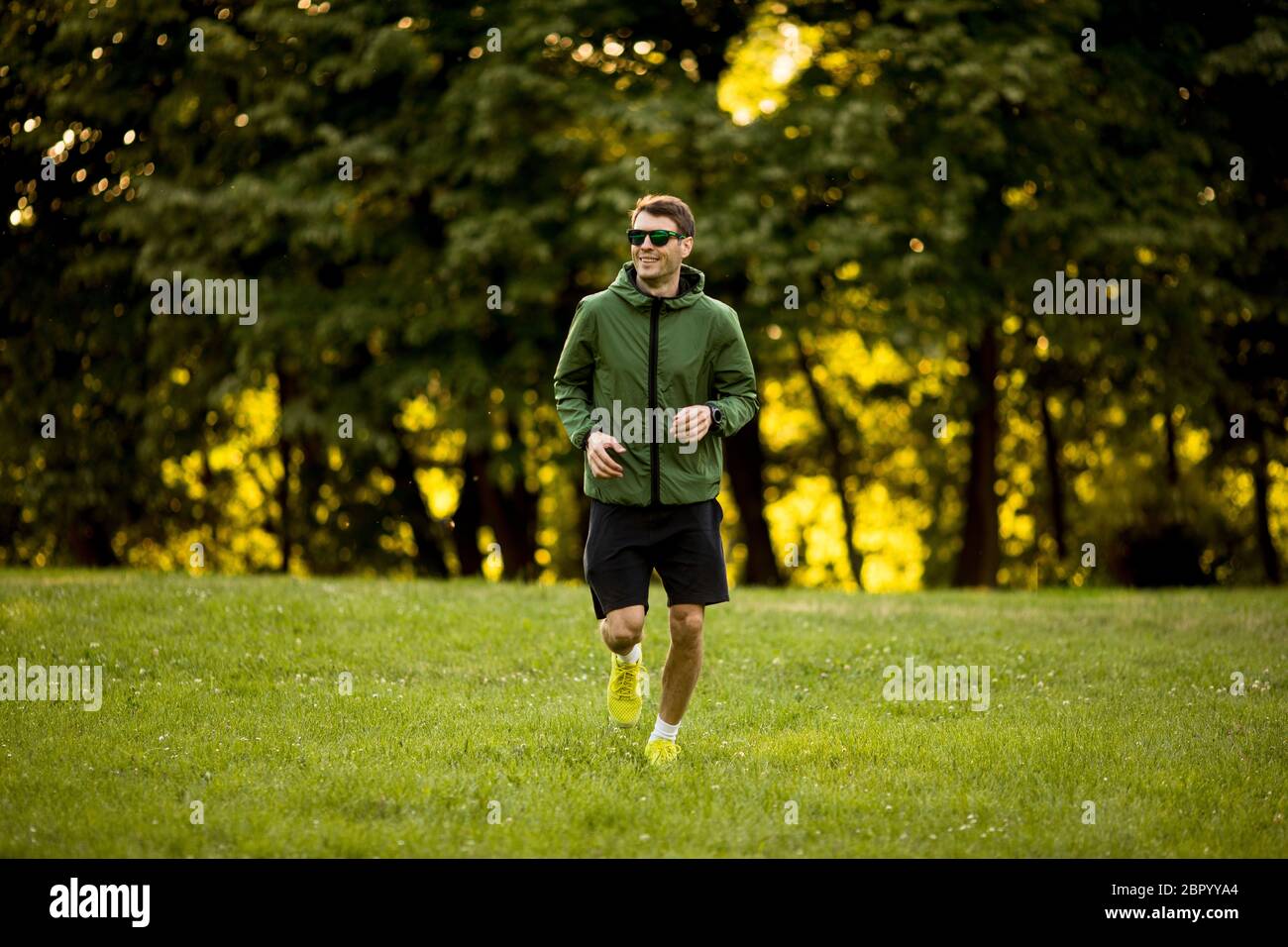 Athletic handsome young man running while doing workout in sunny green ...