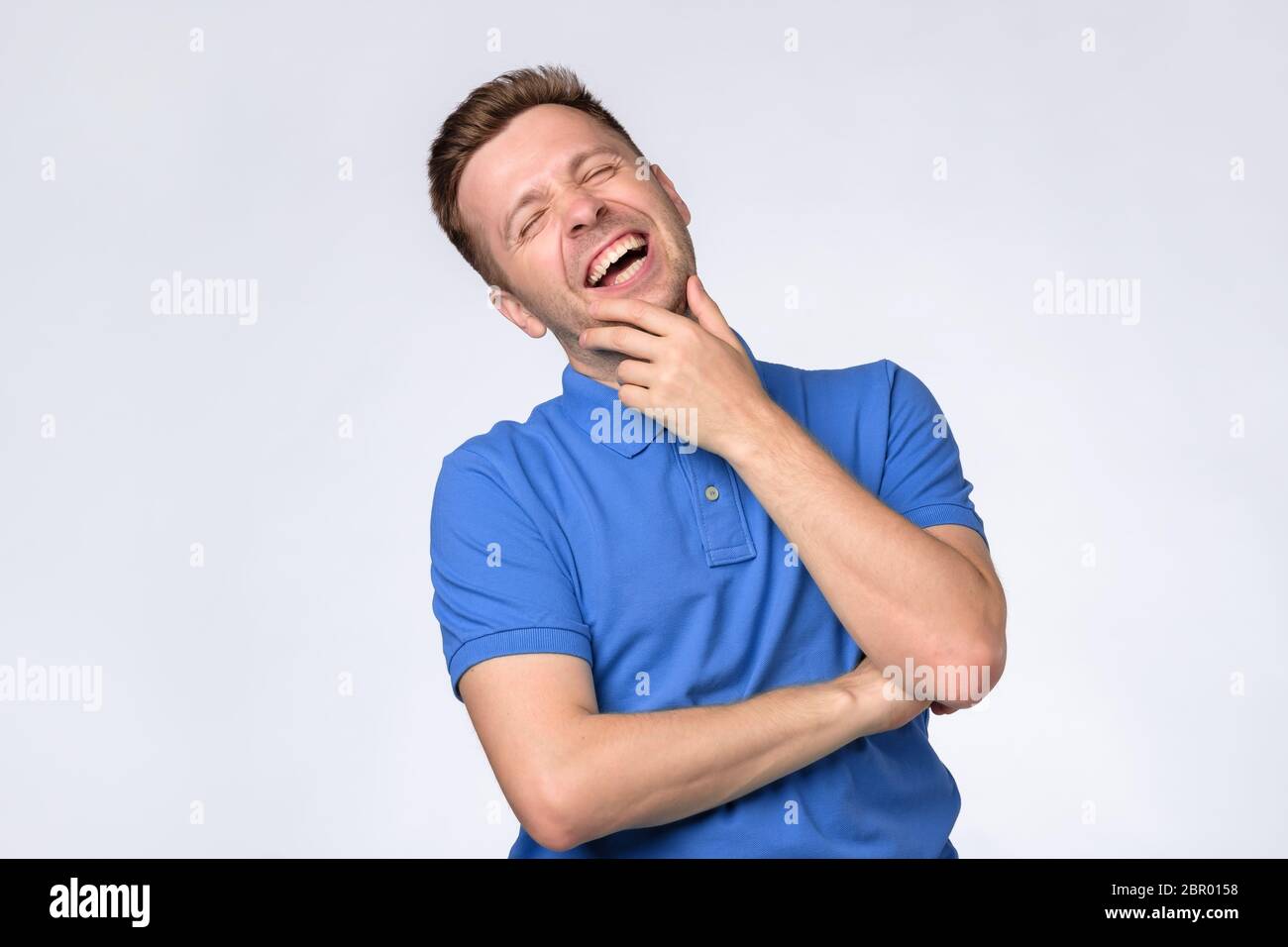 Handsome young man in blue clothes laughing isolated over white ...