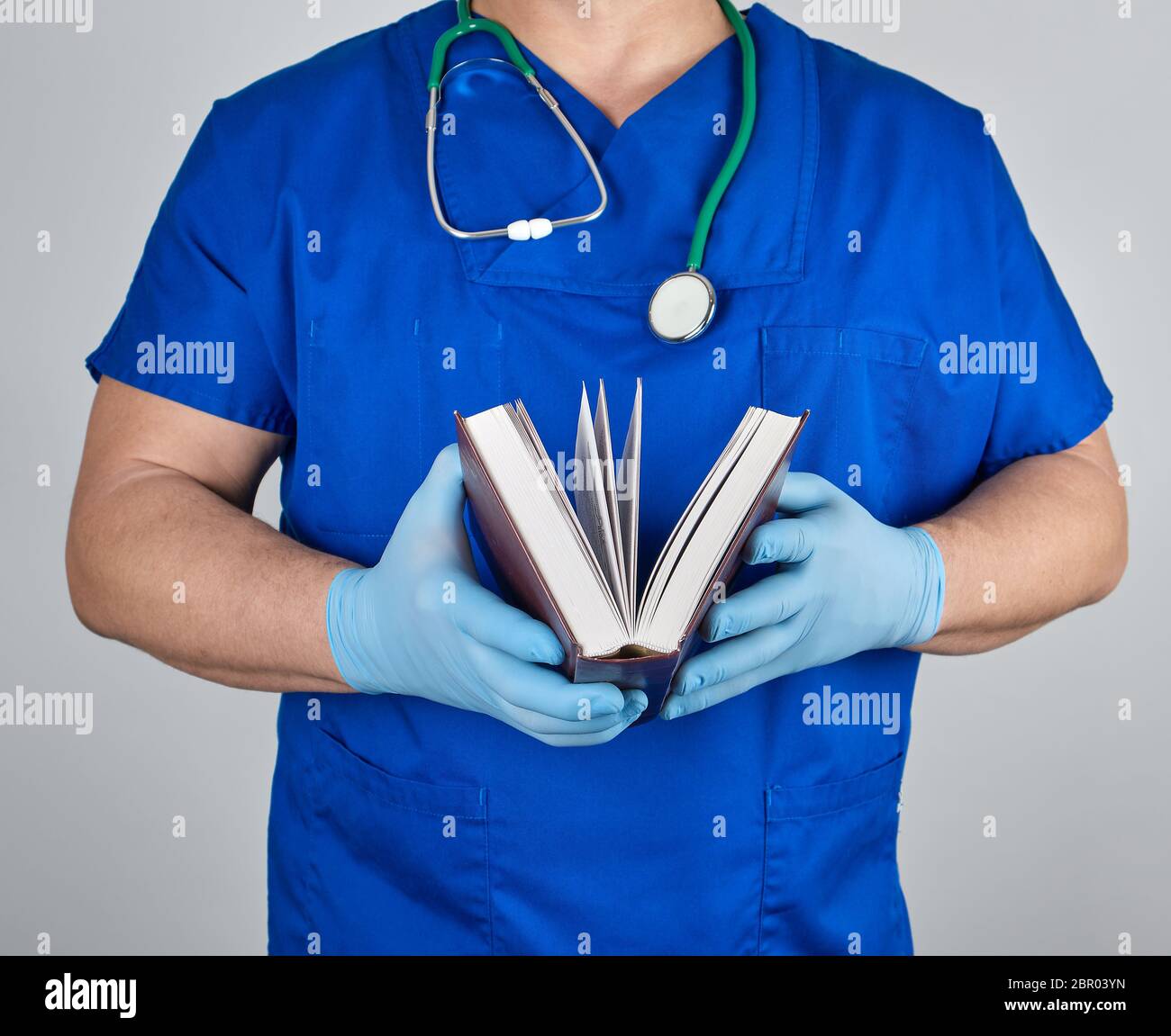 doctor in blue uniform holds an open book in his hands, gray background ...