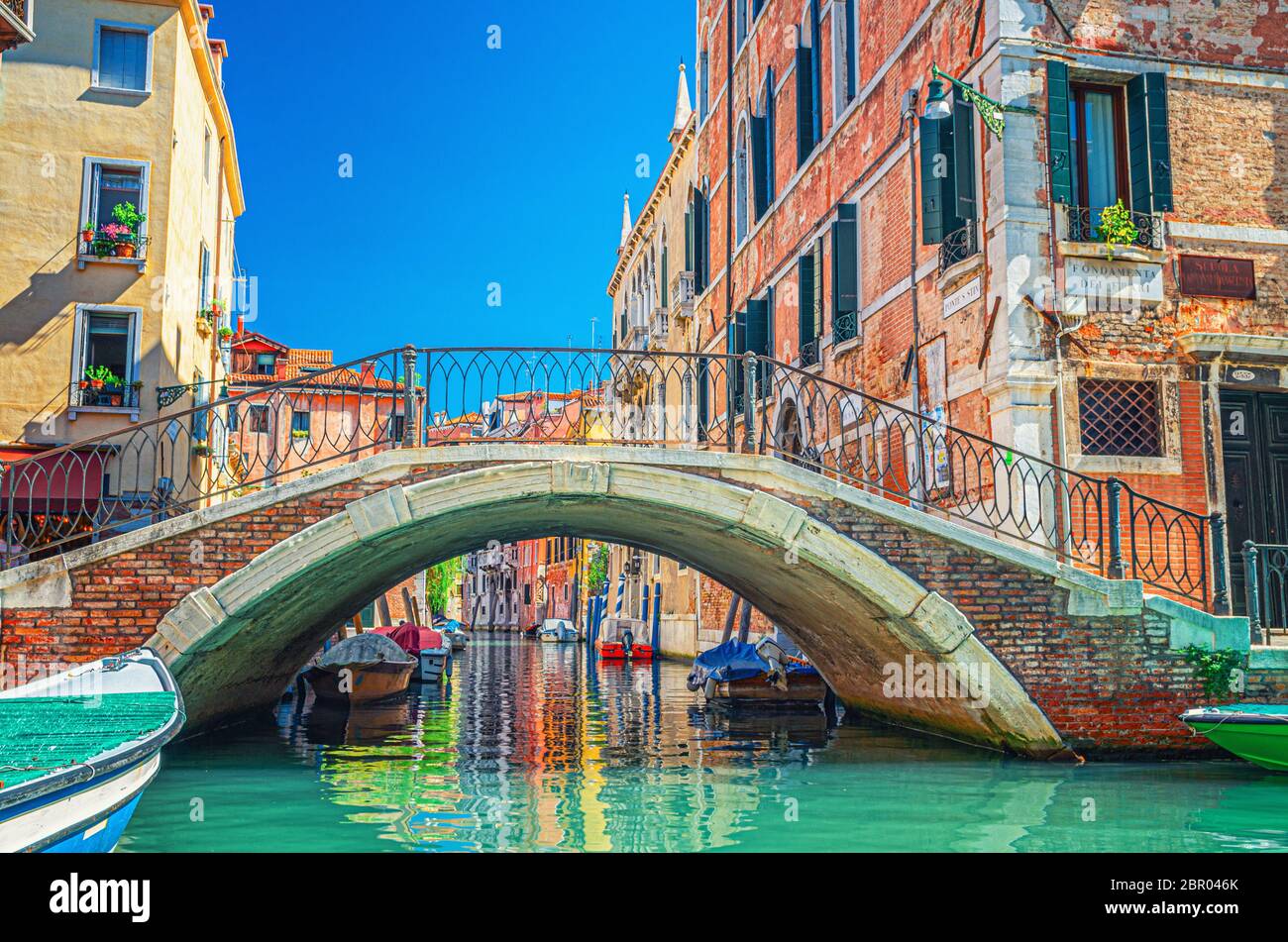 Bridge across narrow water canal in Venice with moored boats between ...