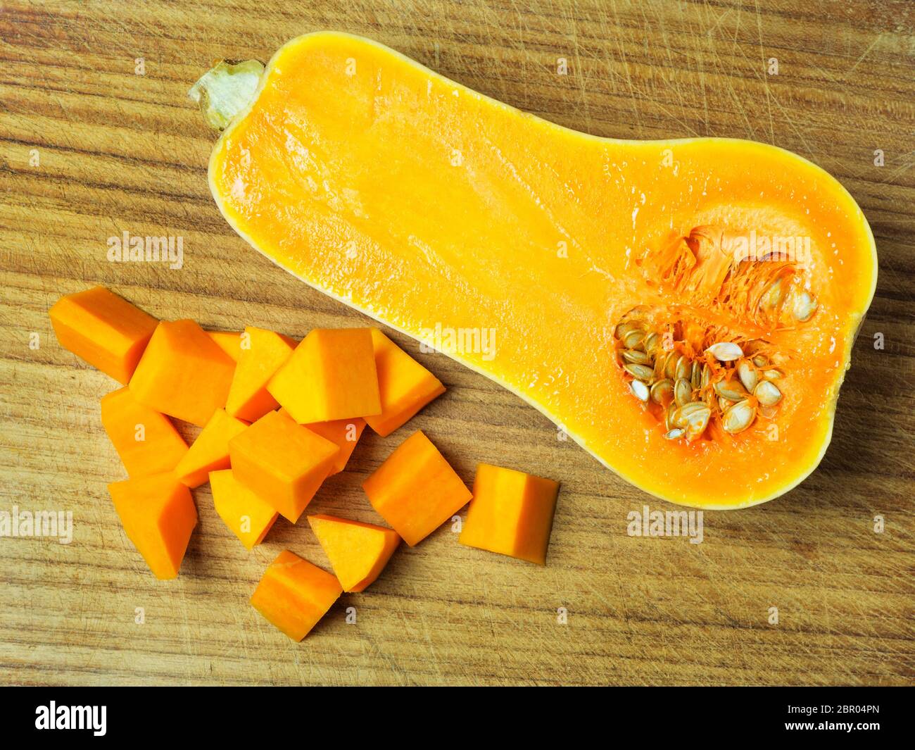 Half a butternut squash with seeds on a wooden chopping board with bit ...