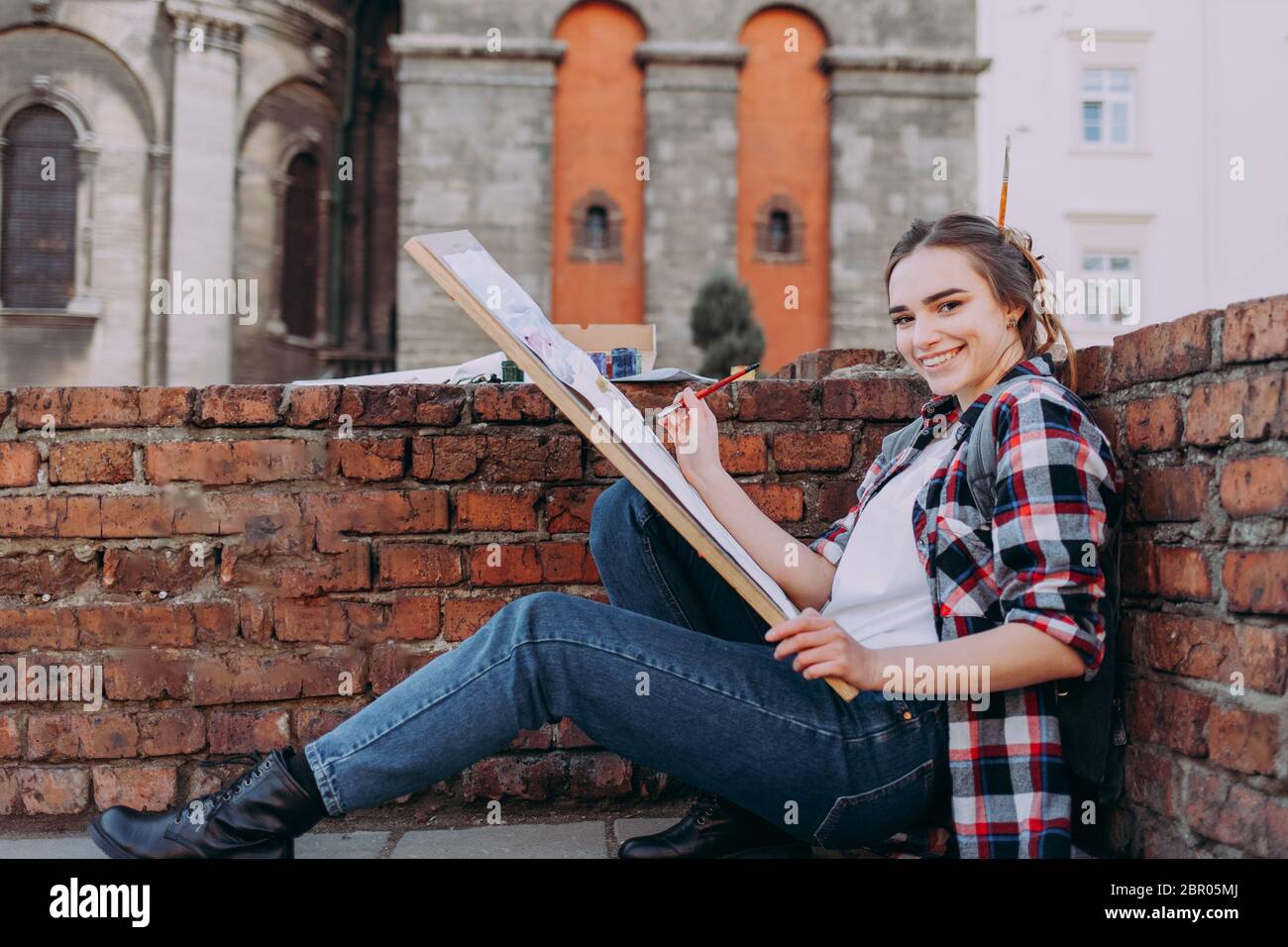 Beautiful girl in a plaid shirt draws old buildings while sitting near ...