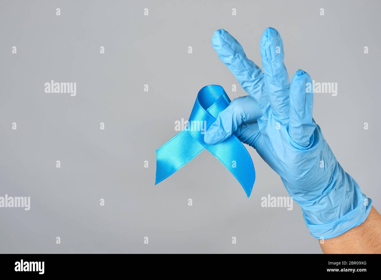 hand in blue latex glove holding a blue ribbon in his hand, a symbol of ...
