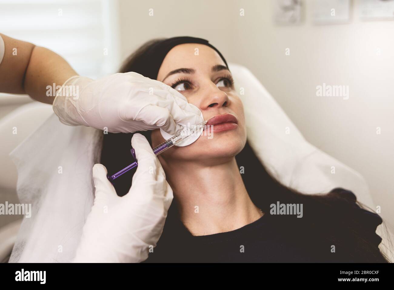 Doctor makes the patient injection of botox on the lips. Woman enlarges ...