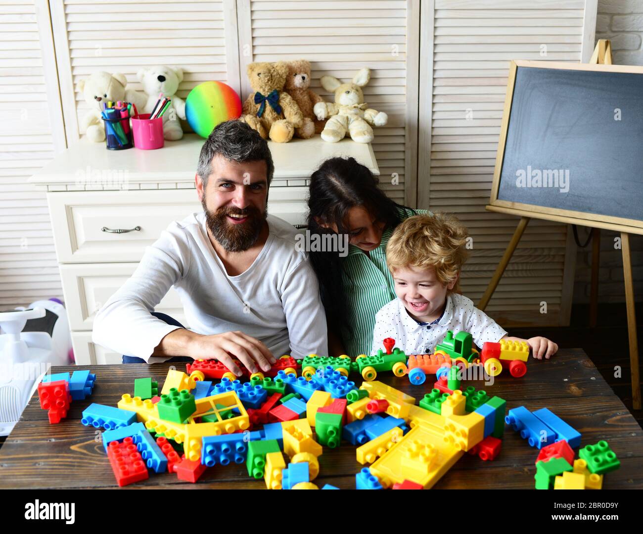 Parents and son with happy faces make brick constructions. Young family ...