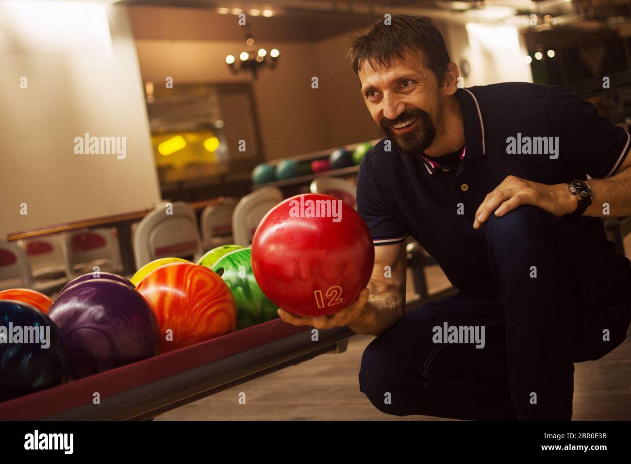 The smiling bowler is playing bowls and holding a red bowling ball in ...