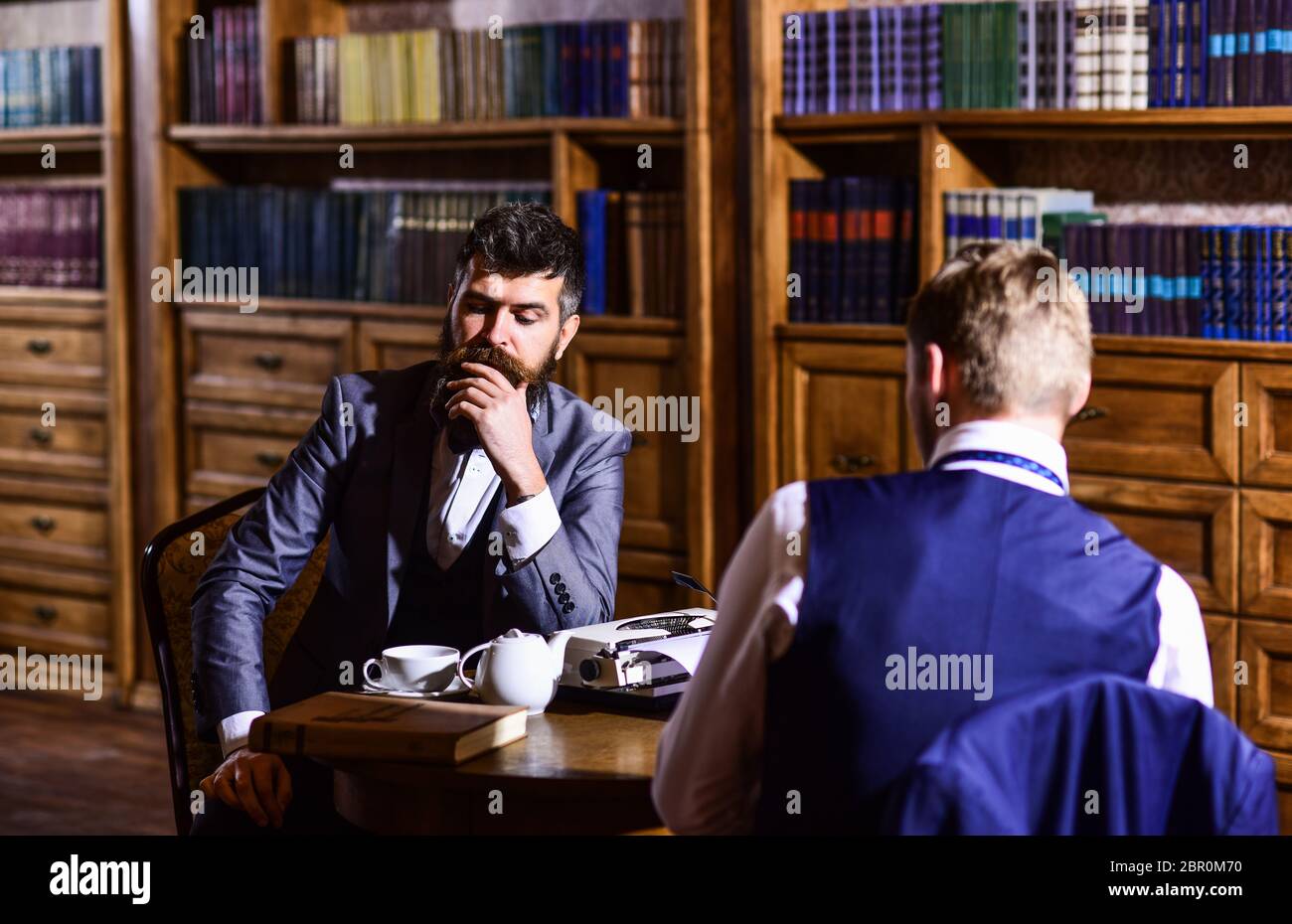 Men in suit with vintage bookshelves on background. Professors speaking ...