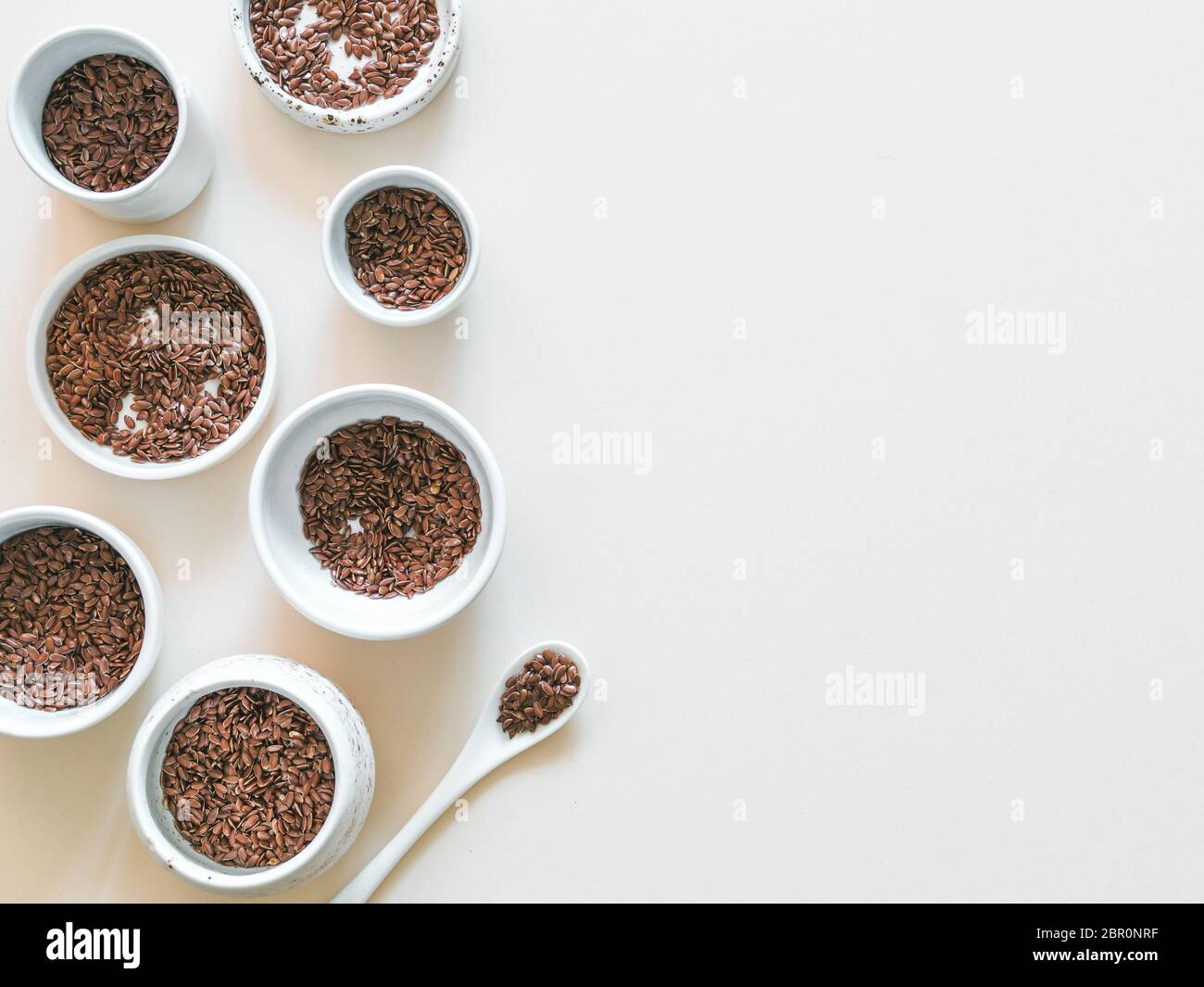 flax seeds on white or light beige background. Set of small bowls with ...