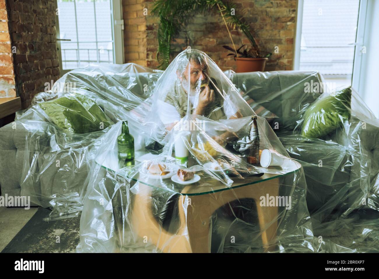 Senior man covered with plastic, eating fast food - environmental ...