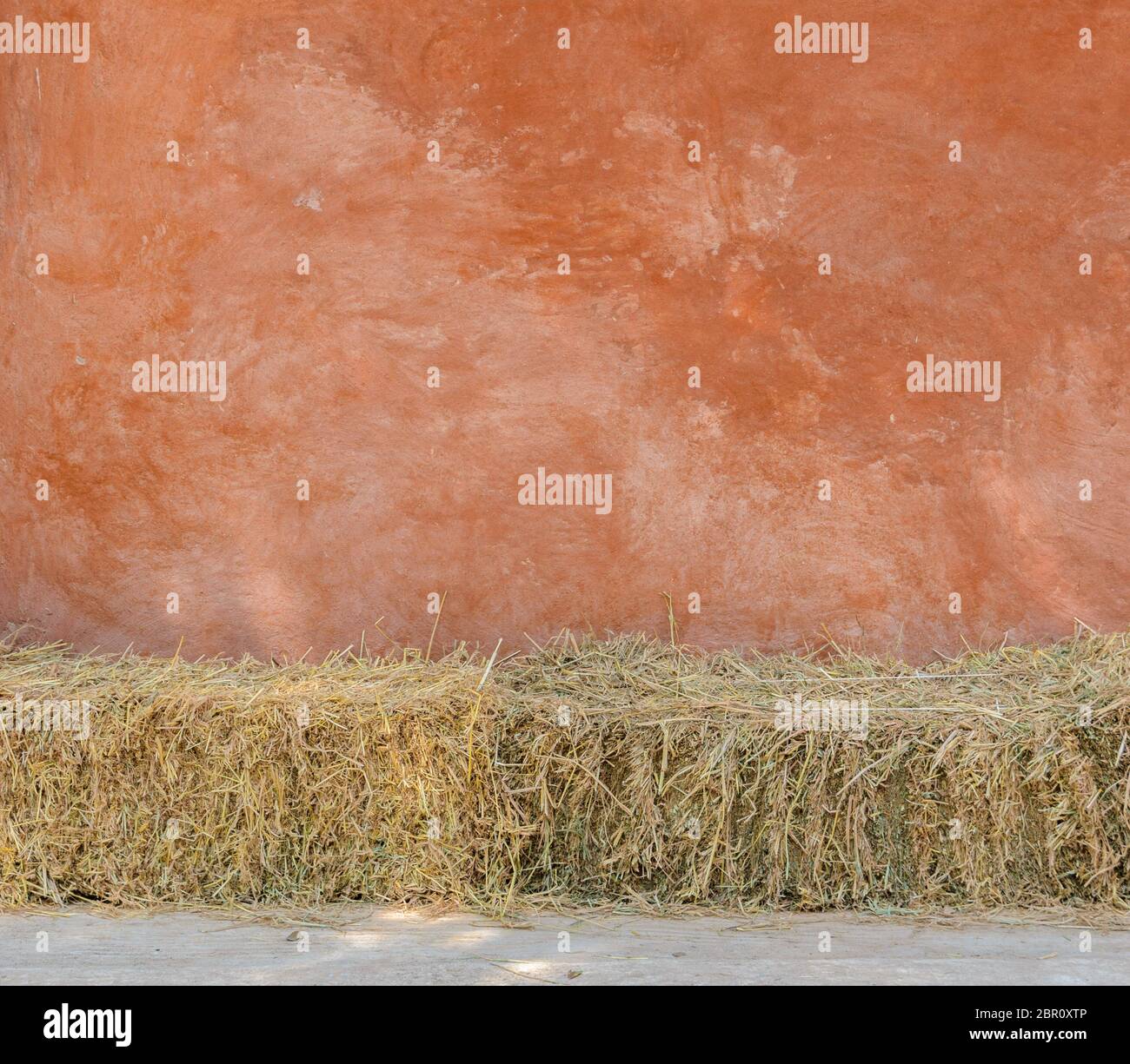 Red natural wall texture of cob house with straw bales as a seat. It is ...