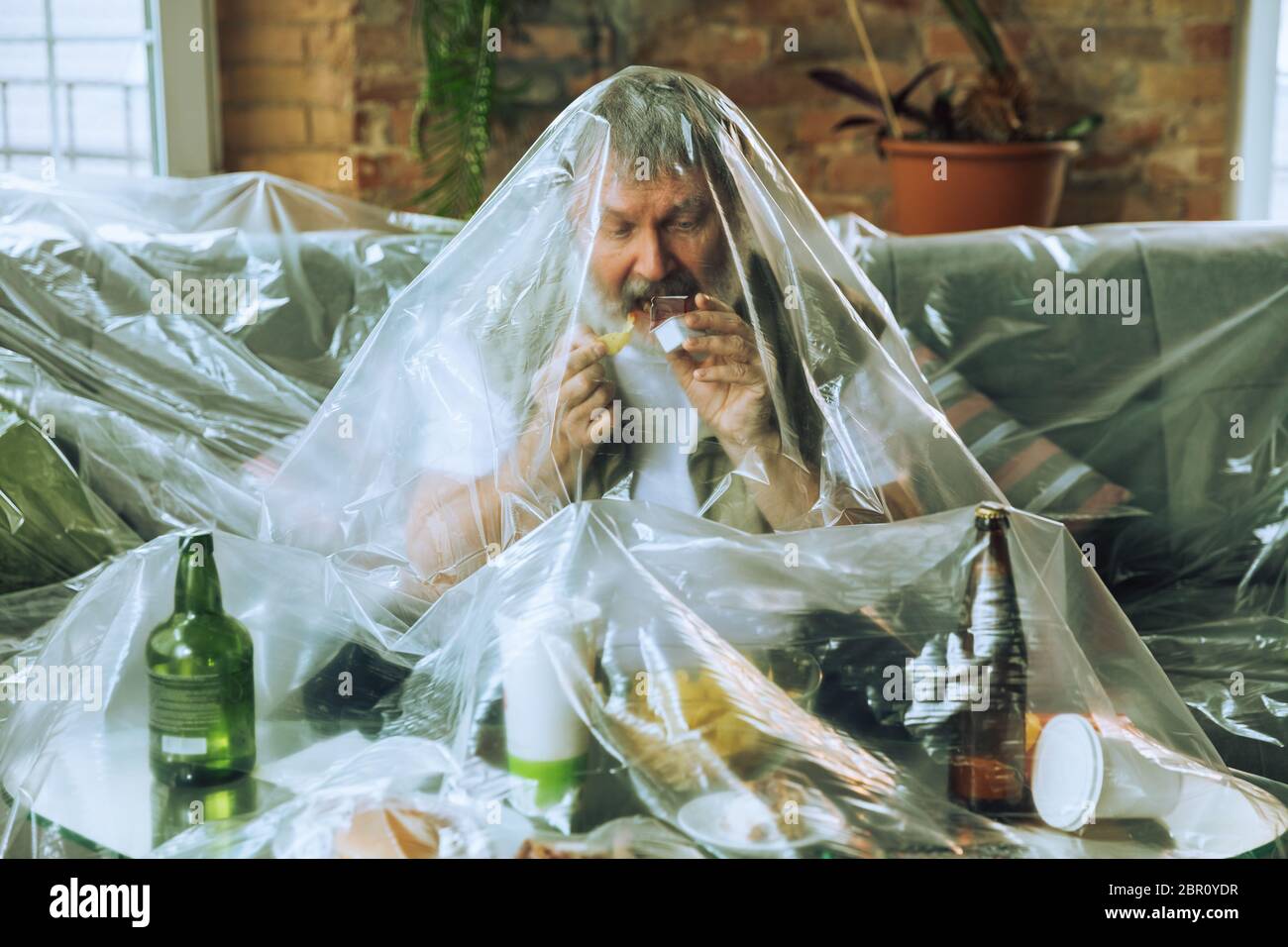 Senior man covered with plastic, eating fast food - environmental ...