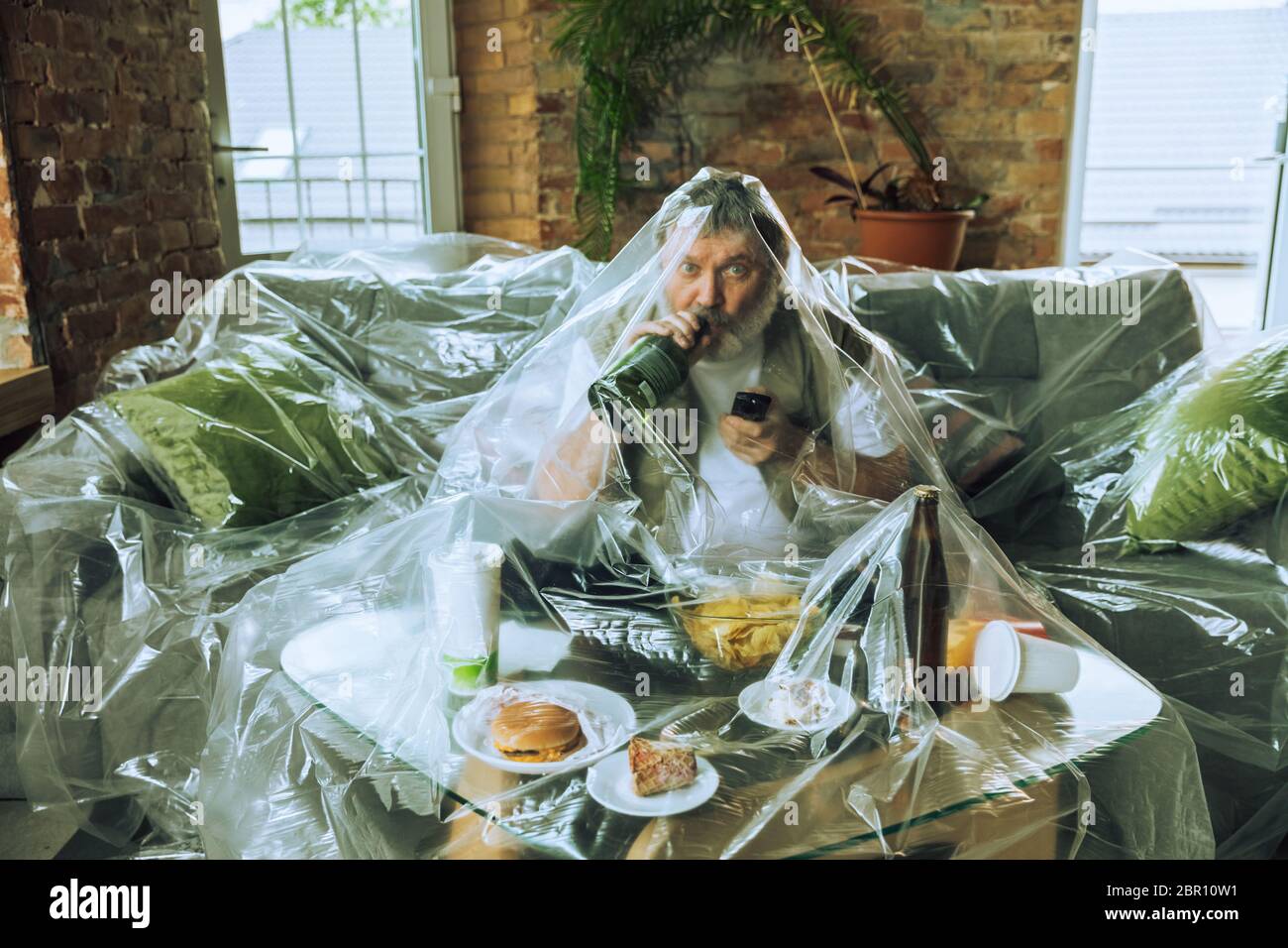 Senior man covered with plastic, eating fast food - environmental ...