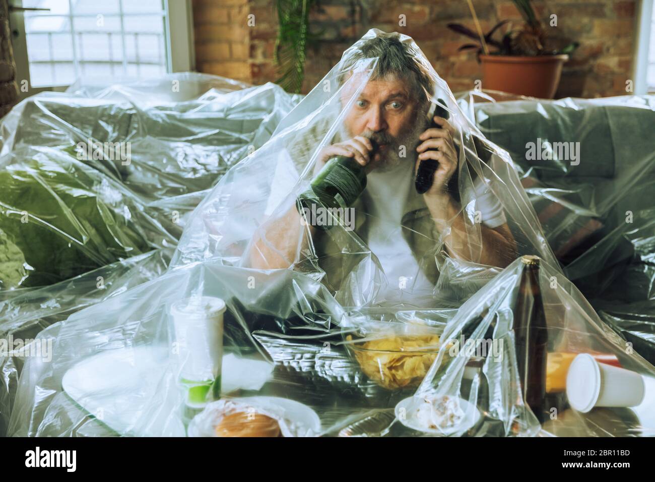 Senior man covered with plastic, eating fast food - environmental ...