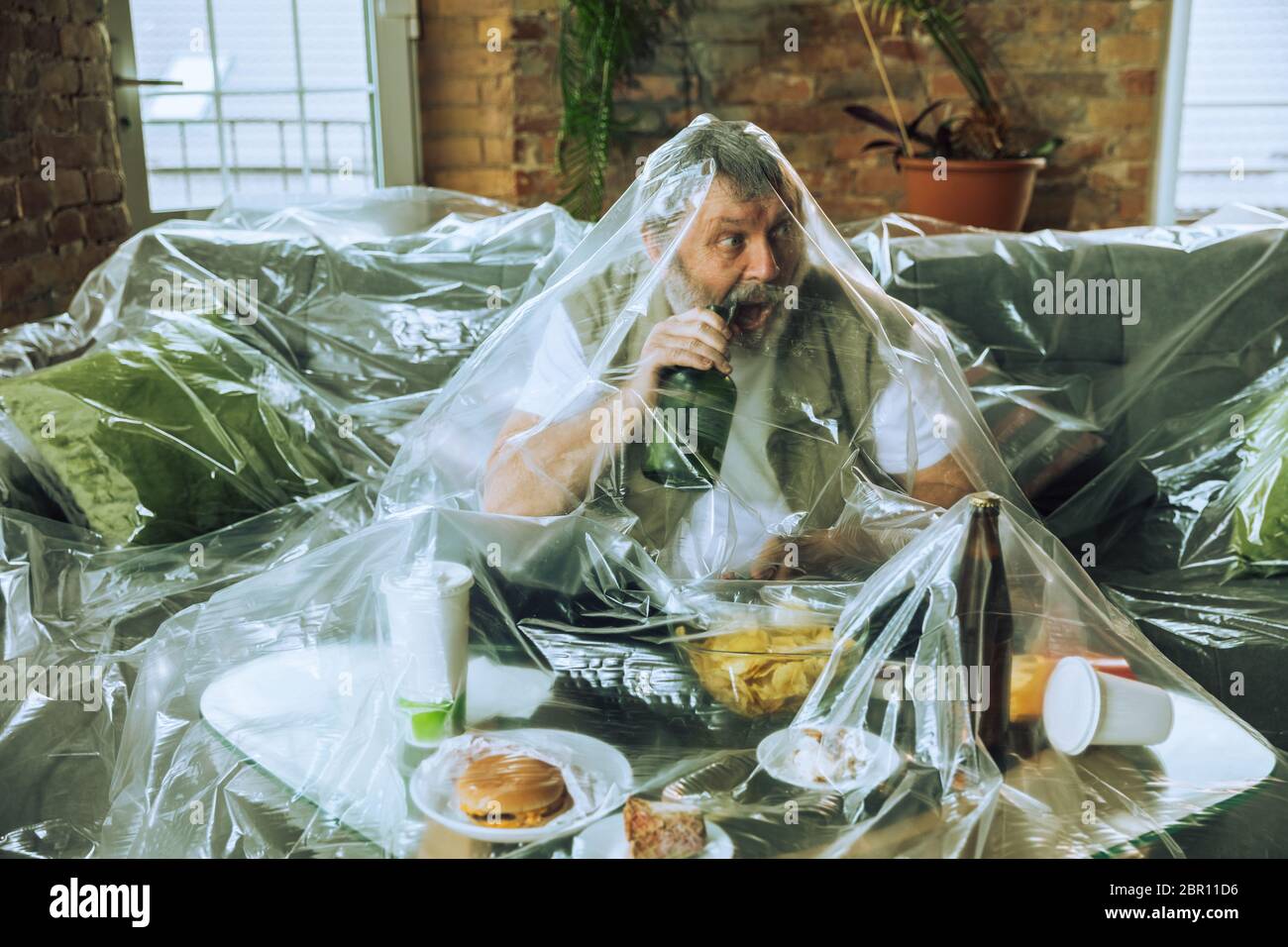 Senior man covered with plastic, eating fast food - environmental ...