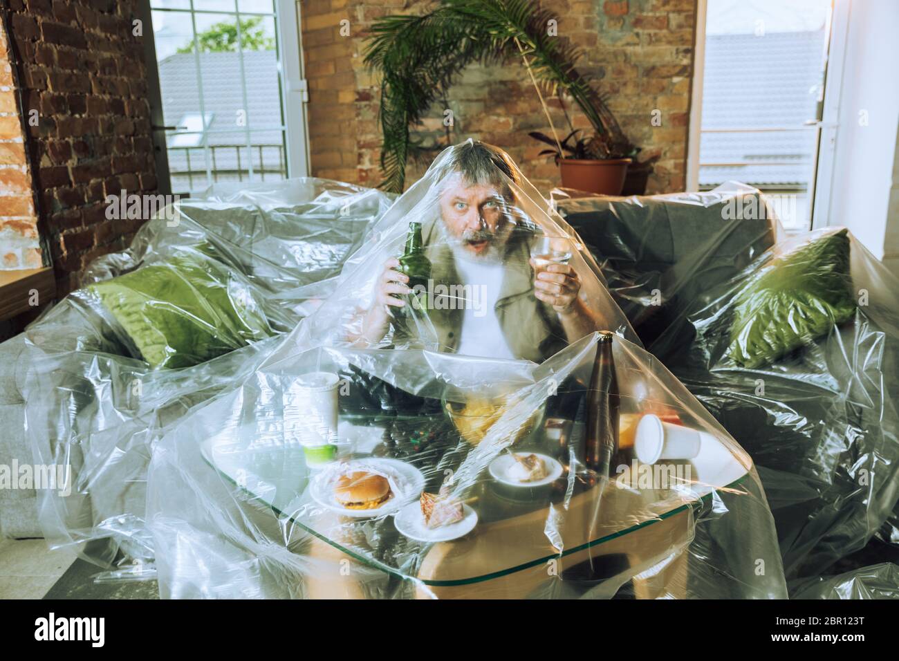 Senior man covered with plastic, eating fast food - environmental ...