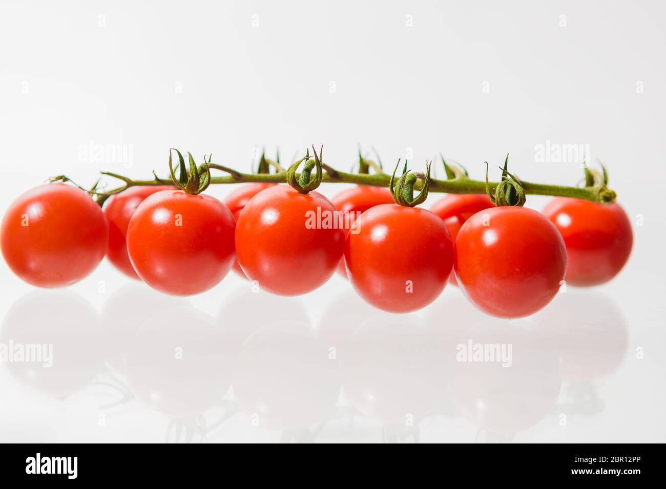 Small red Cherry tomatoes are lying branch isolated on white background ...
