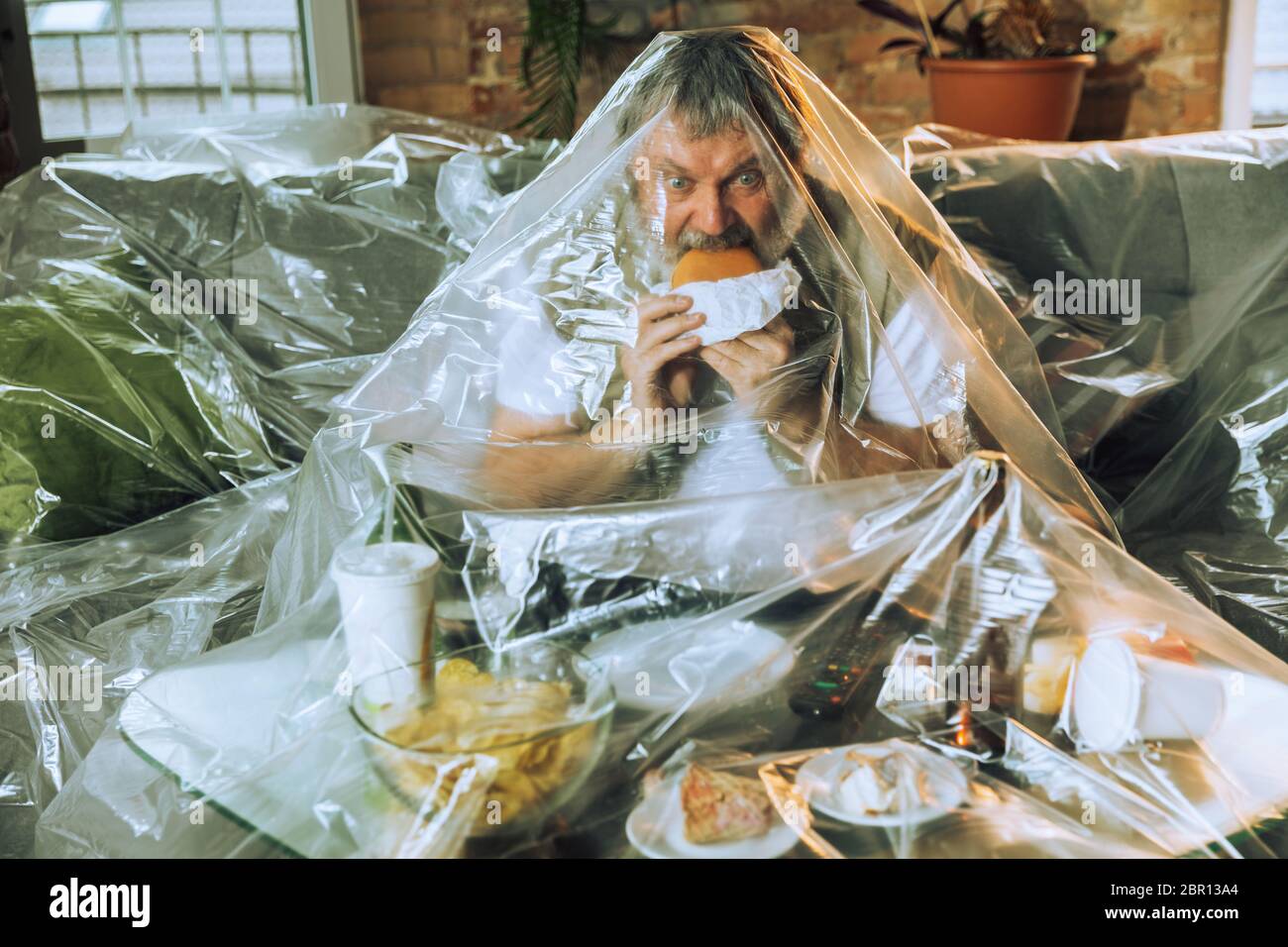Senior man covered with plastic, eating fast food - environmental ...