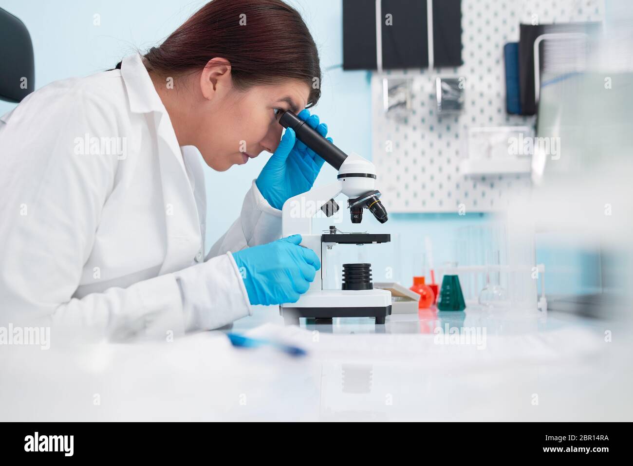 Female epidemiologist looking through microscope in laboratory ...